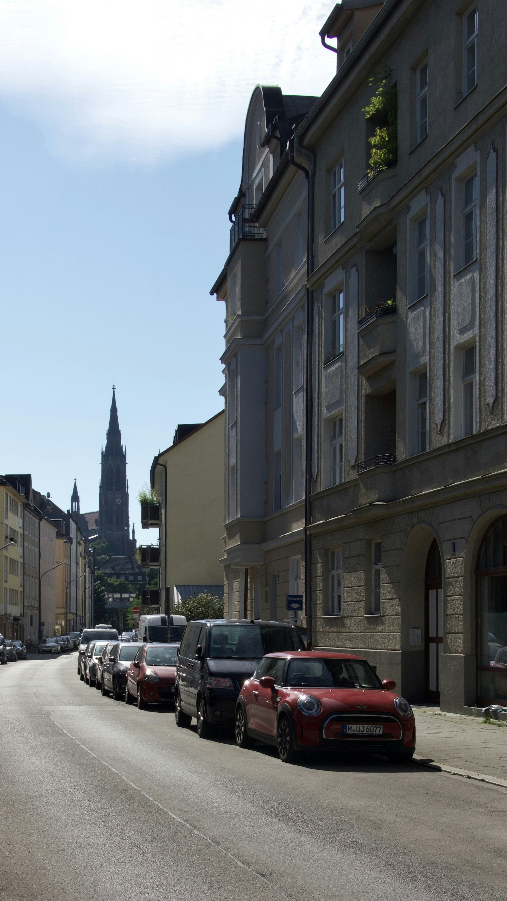 Charming street scene showcasing a row of parked cars with a historic church spire rising in the background against a clear blue sky.