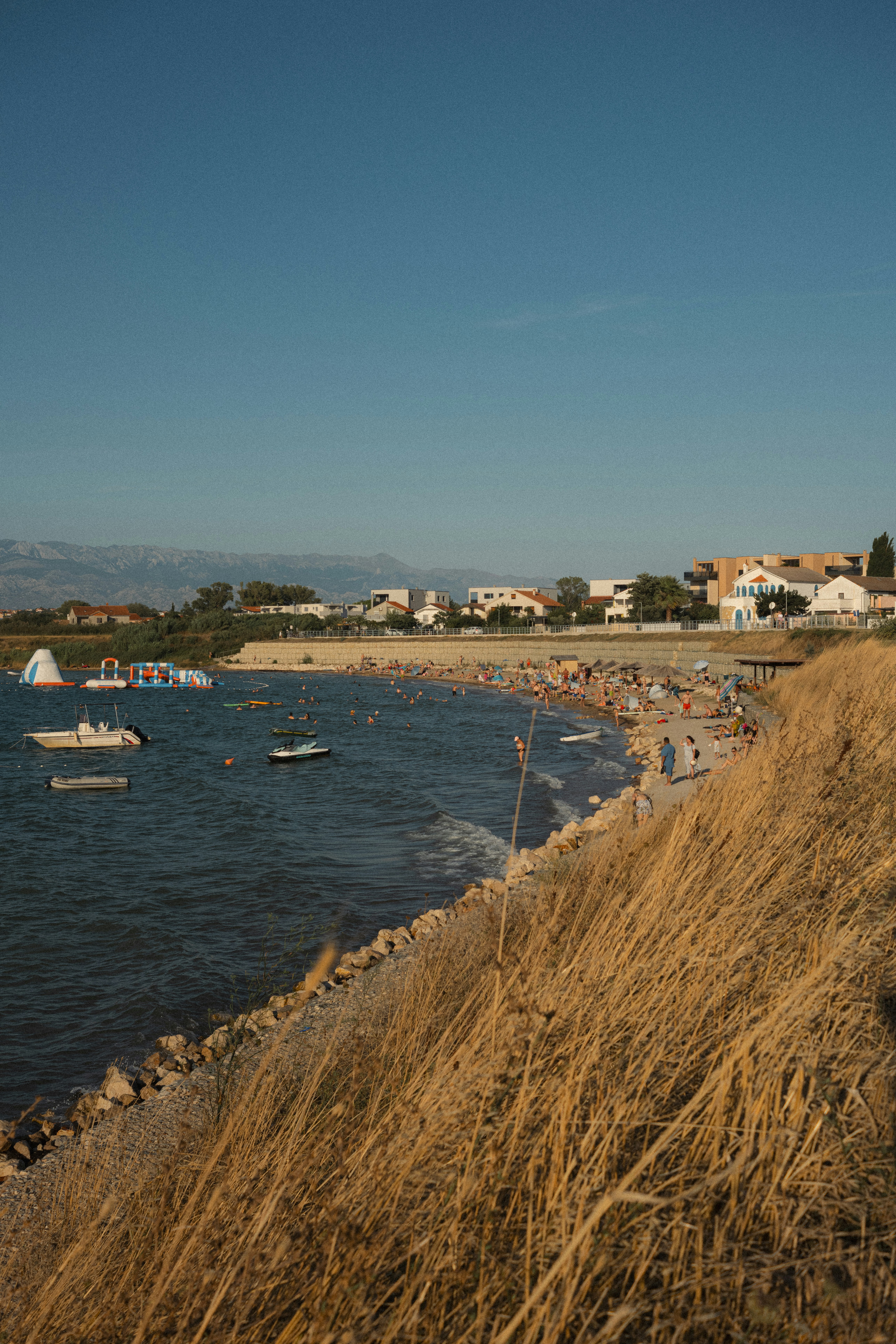 Crowded beach with inflatable water toys and distant buildings.