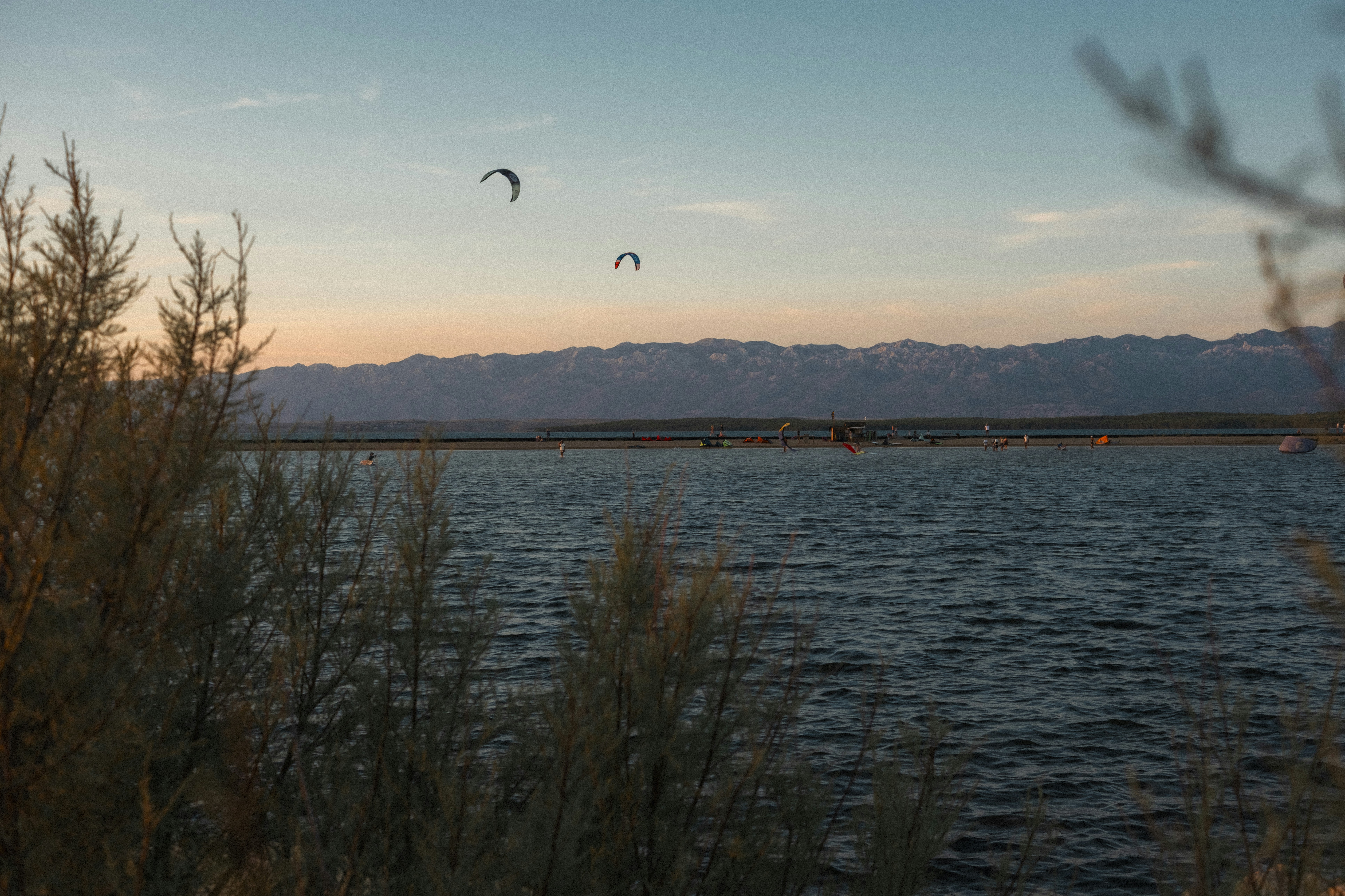 Kitesurfers enjoy the water at sunset with mountains in background