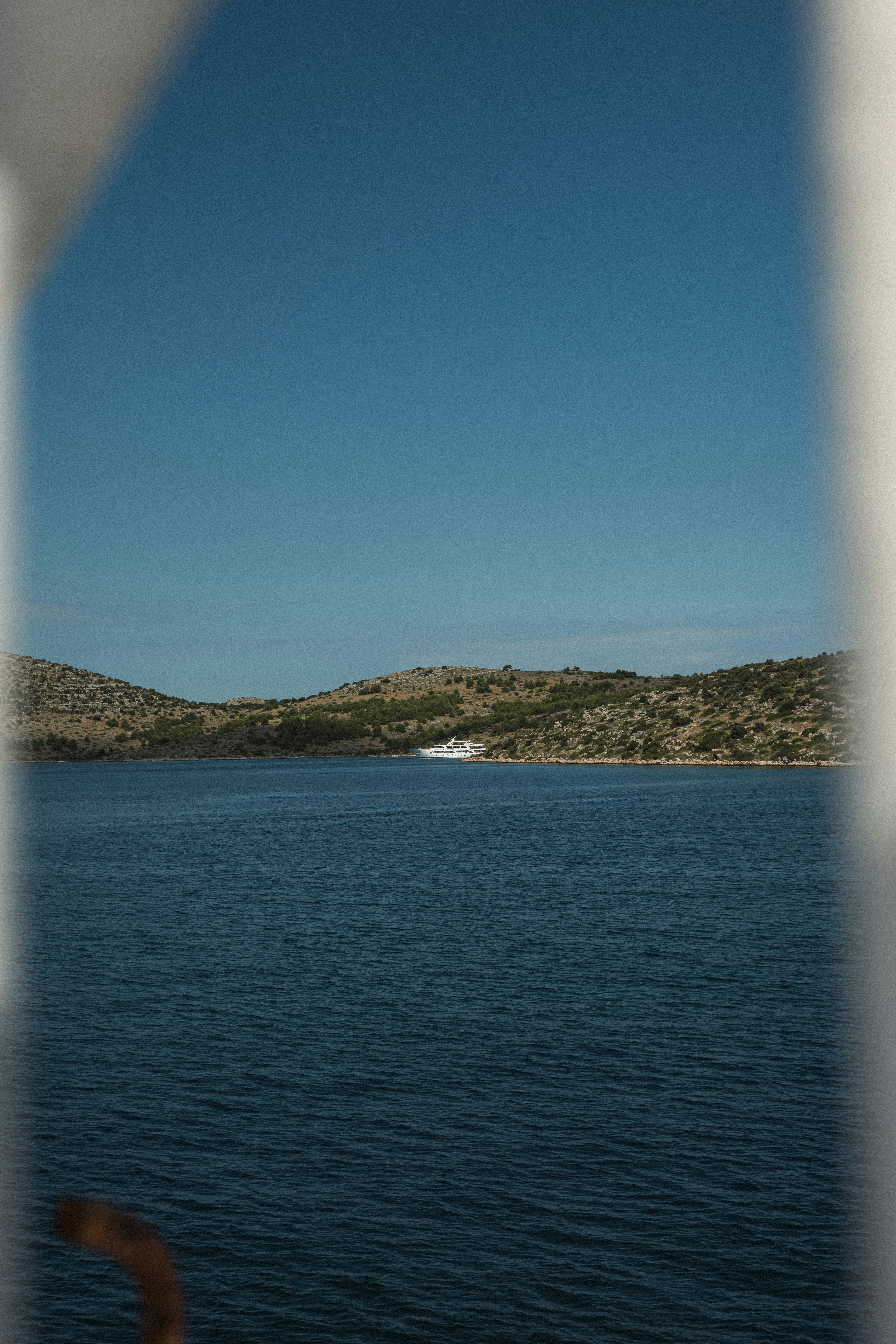 Through a Narrow Frame, a White Yacht Anchors a Quiet Coastal Bay