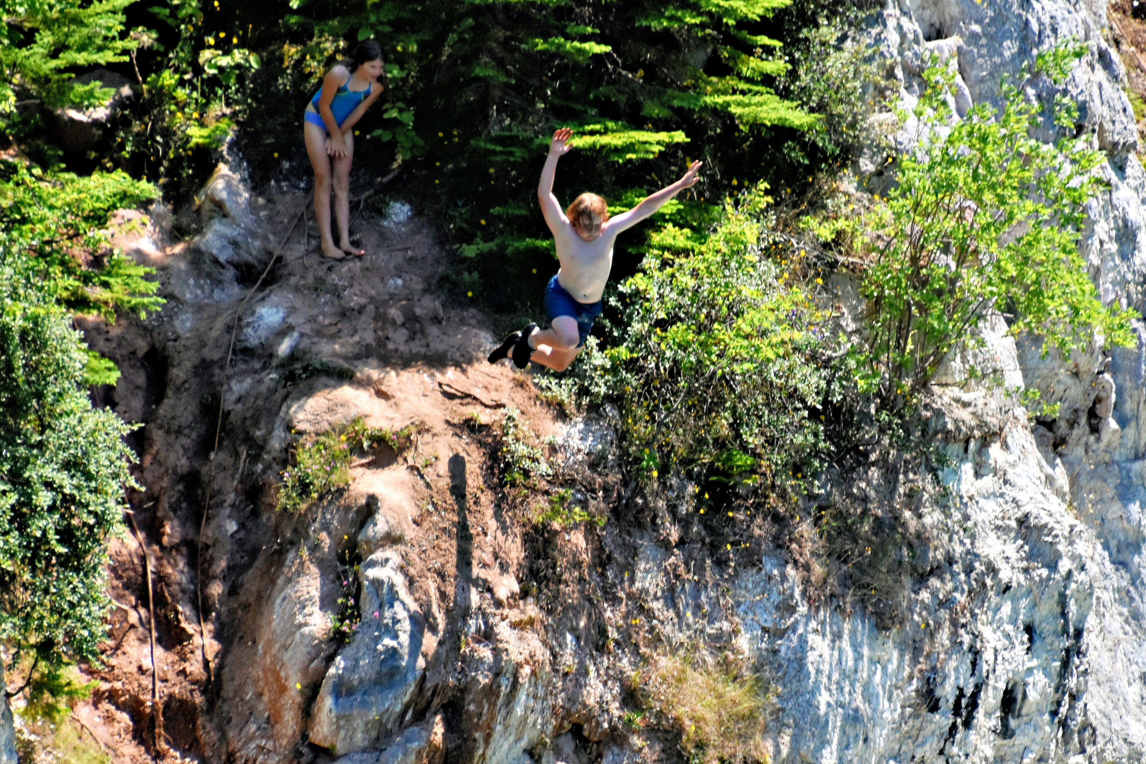 Man jumps off cliff into water with friend watching