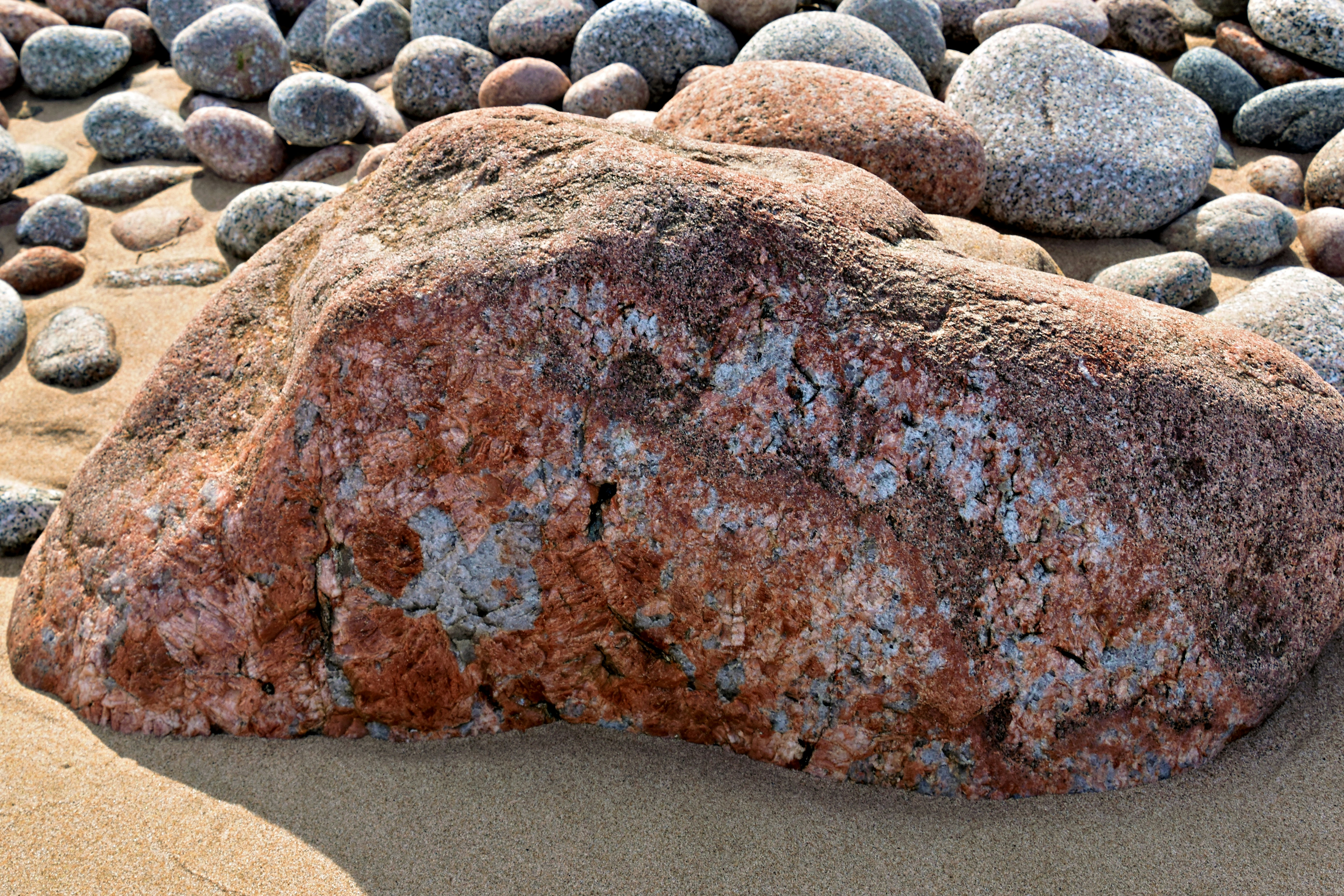 Large reddish-gray boulder on a sandy beach.