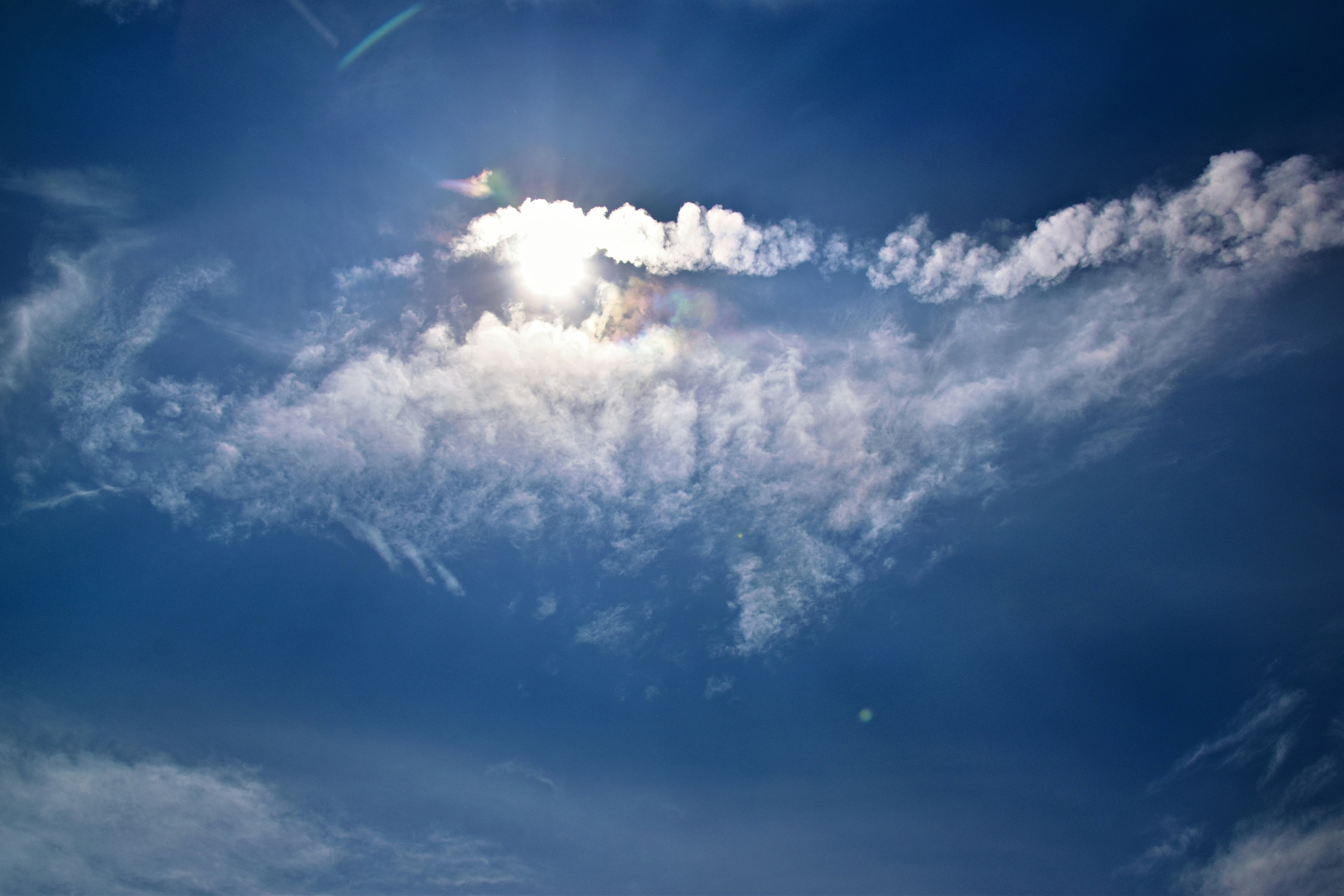 Bright sun peeking through wispy clouds against a vibrant blue sky.