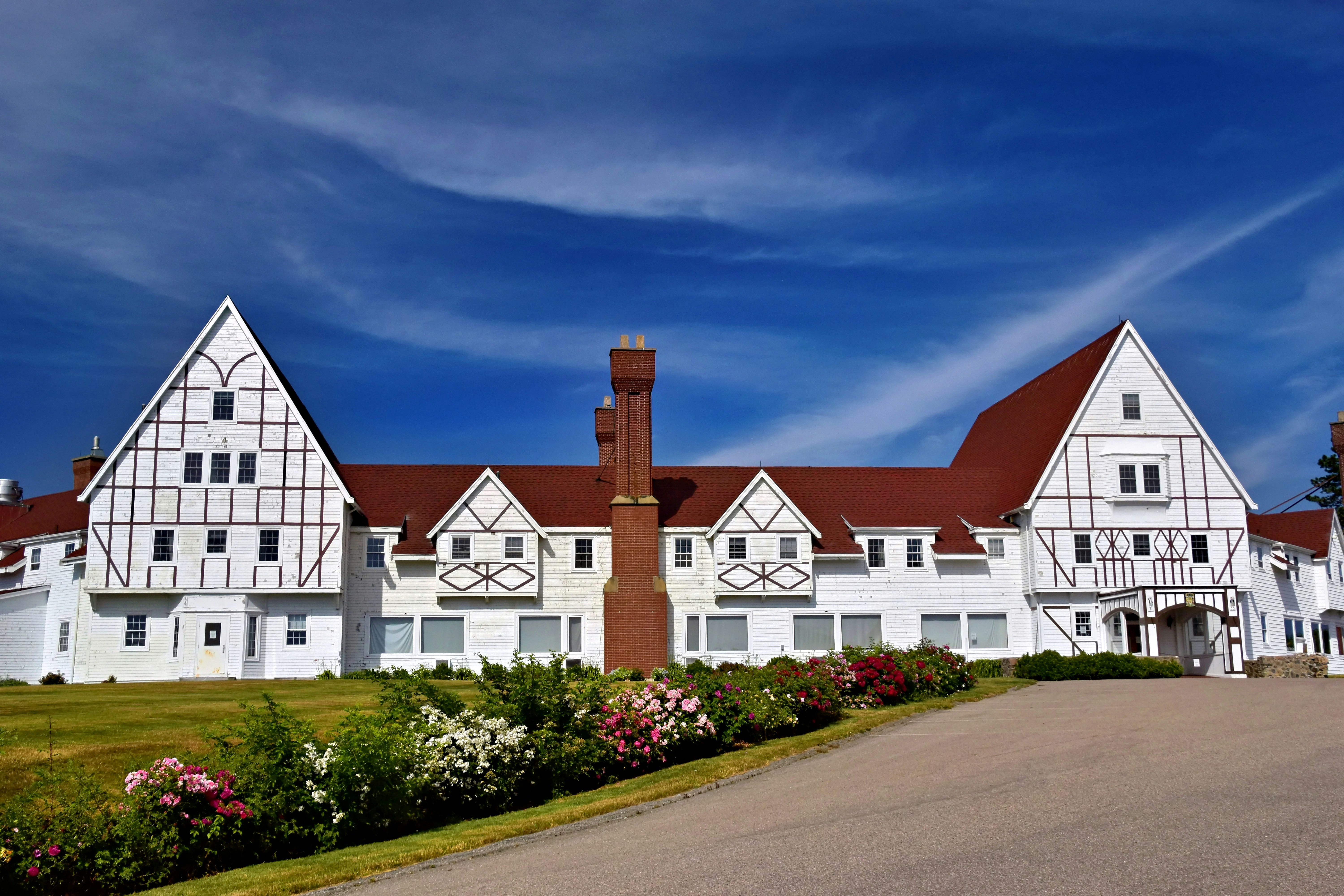 Historic building featuring traditional architecture with a striking red roof and white exterior, surrounded by vibrant flower beds.