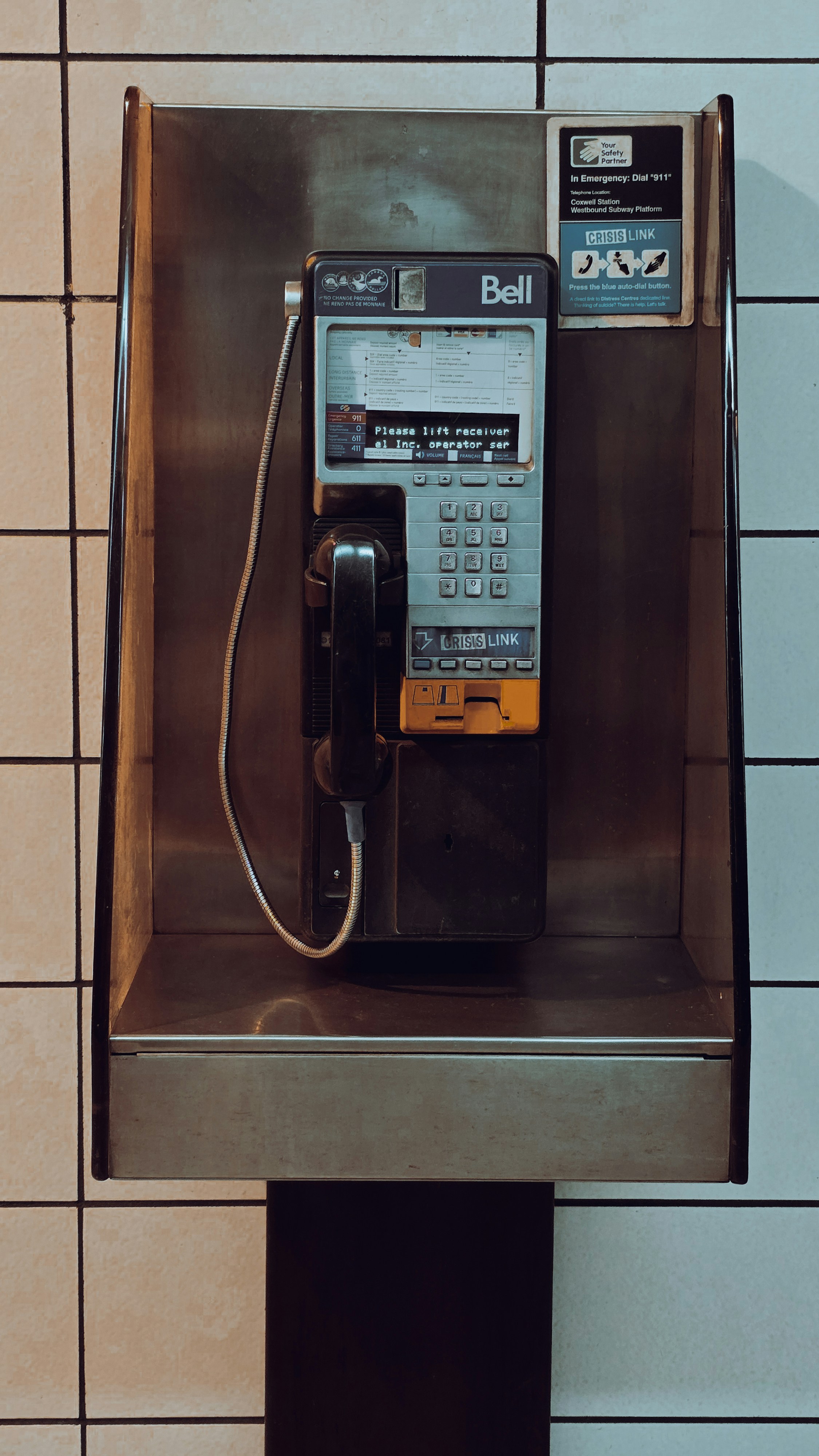 A vintage bell payphone mounted on a tiled wall.