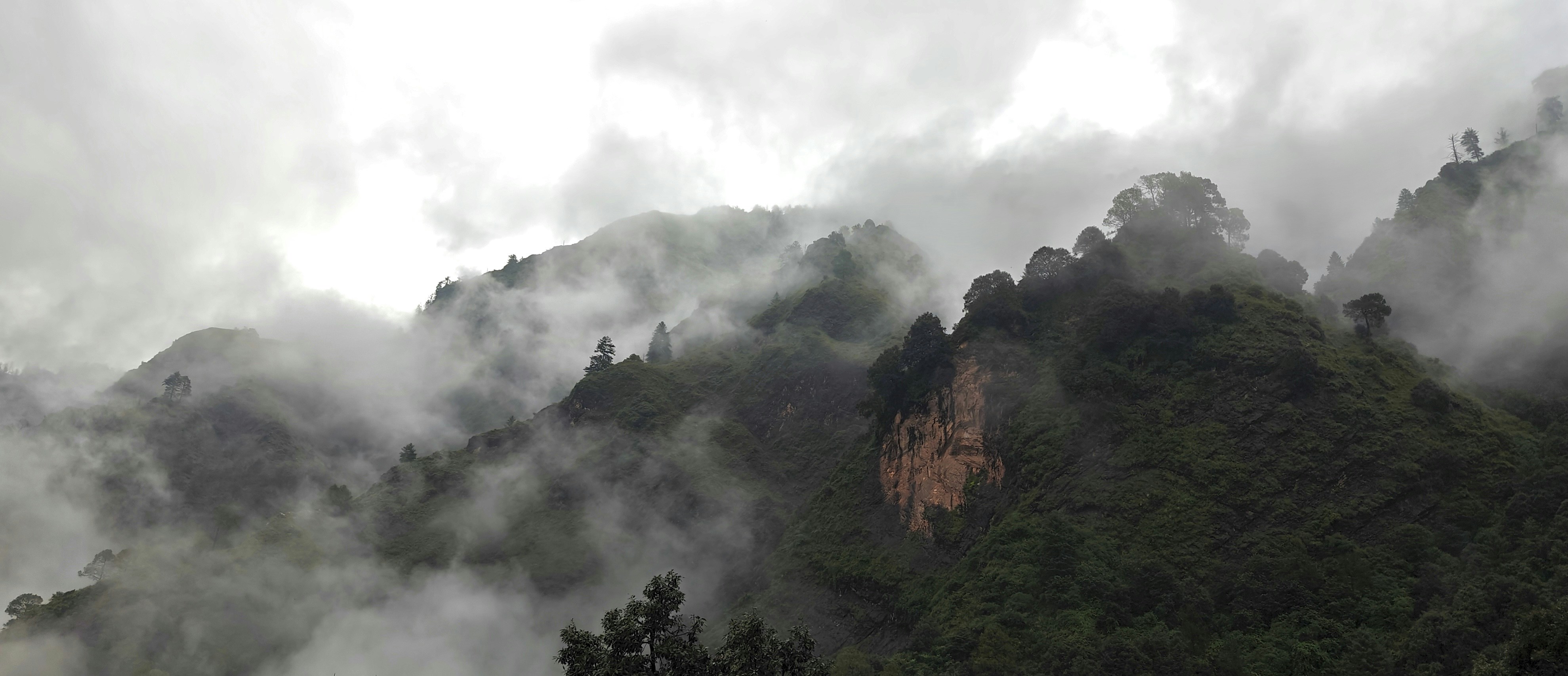 A huge lush green mountain range covered in clouds | Misty mountains covered in green trees and fog