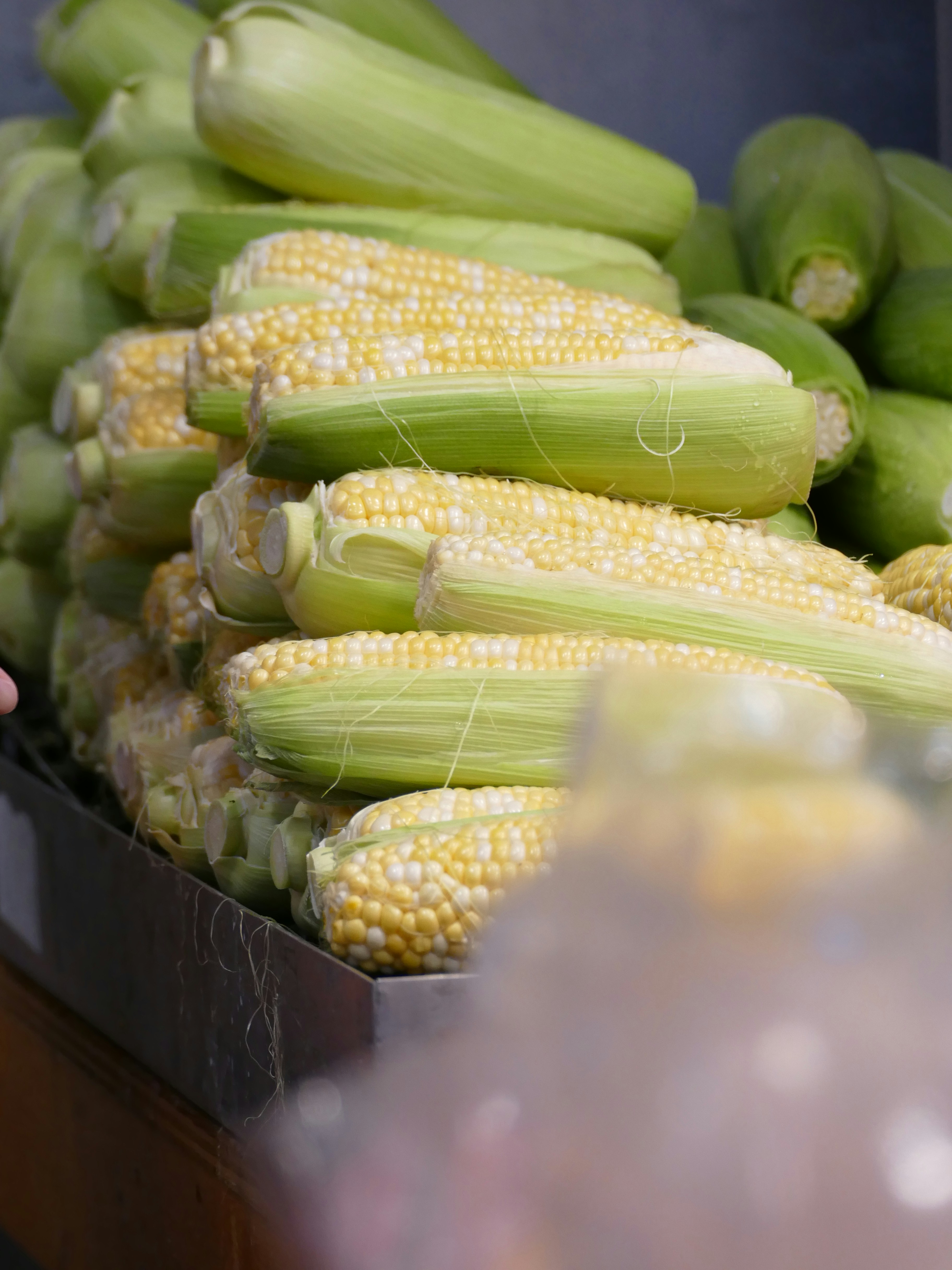 Freshly harvested corn cobs stacked neatly at a market, showcasing their vibrant yellow kernels and green husks.