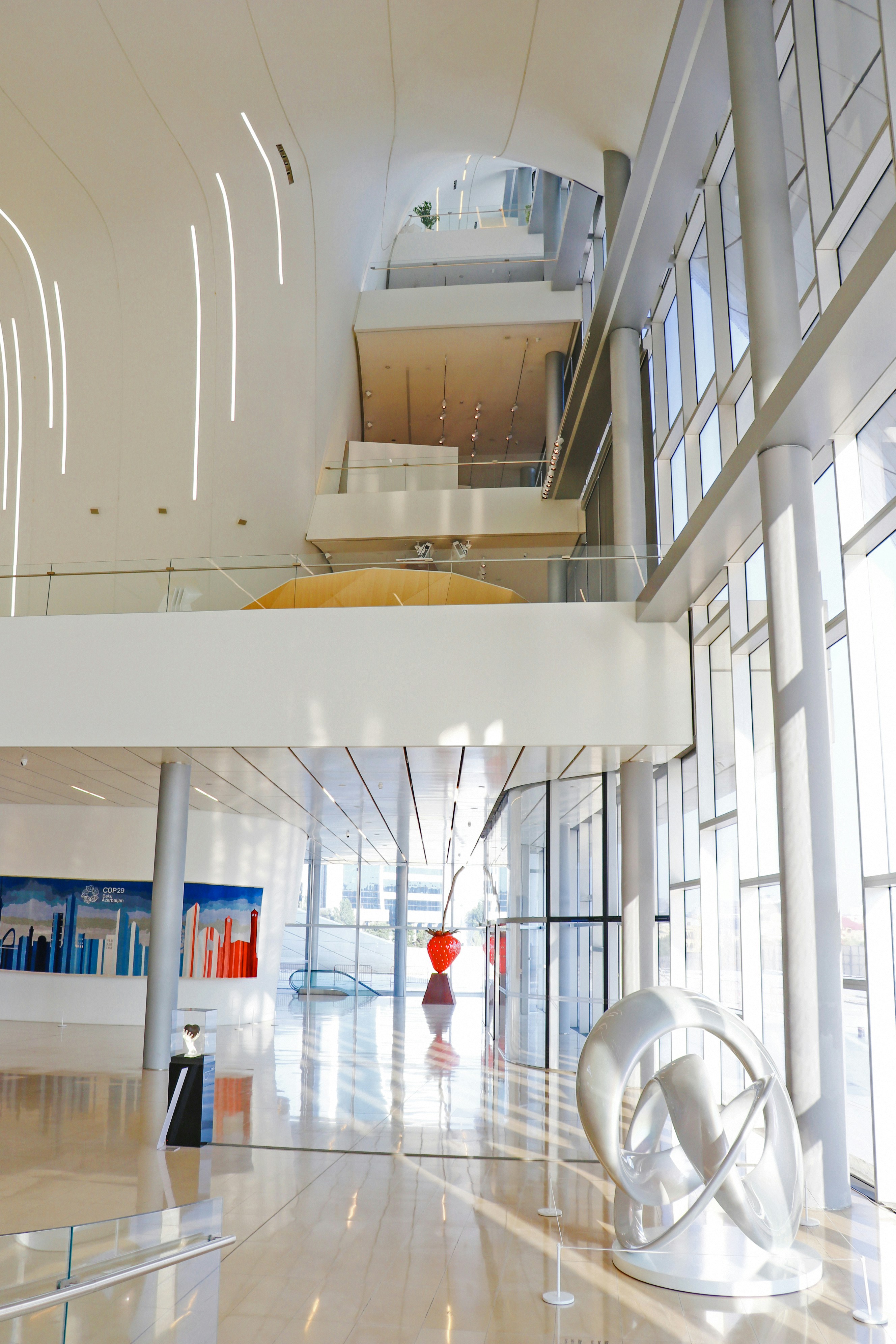 Interior view of a contemporary building showcasing sleek lines, large windows, and artistic sculptures. Natural light floods the space, enhancing the architectural features.