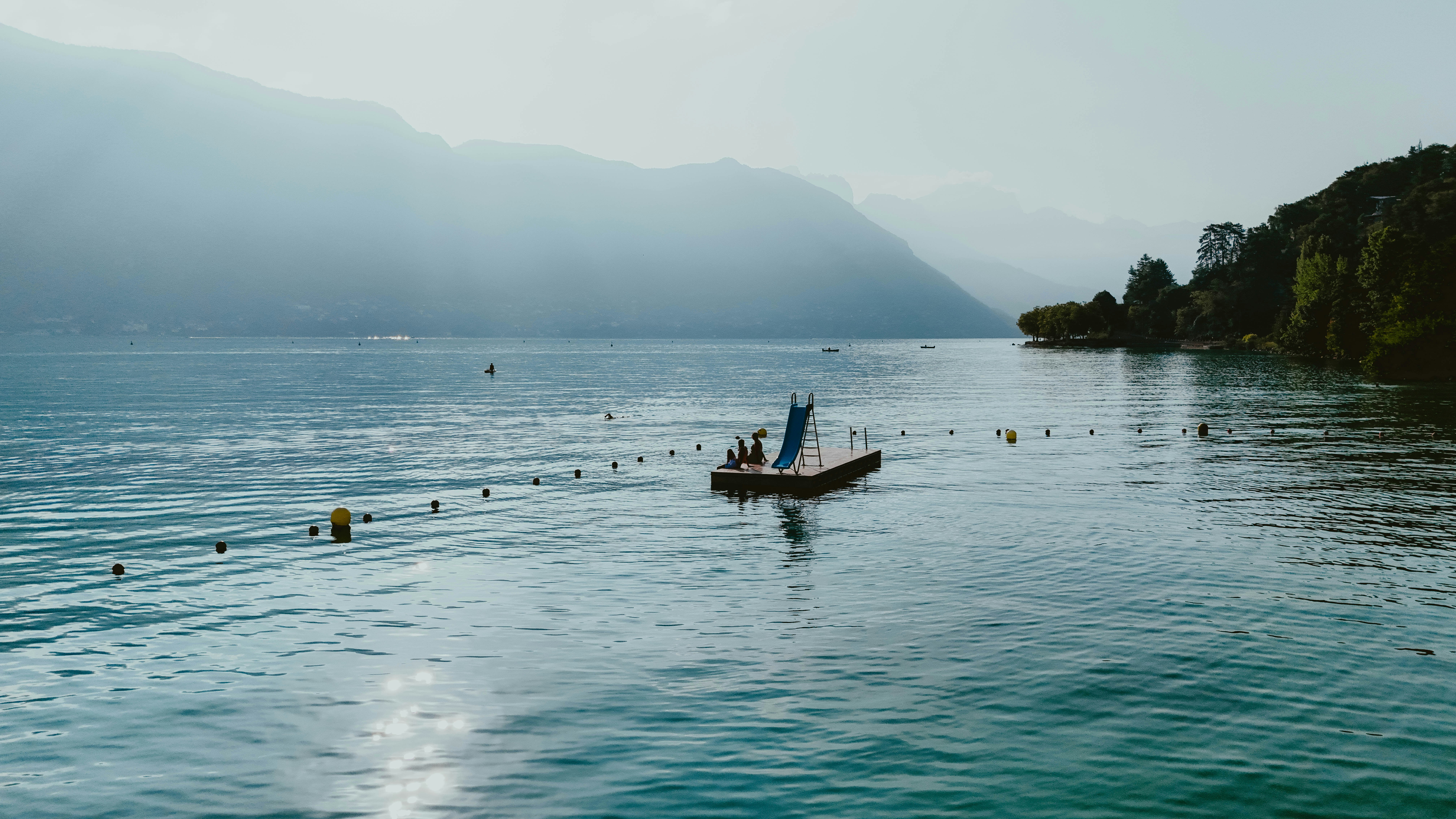 A tranquil scene featuring a dock with people enjoying the calm waters of a lake, surrounded by misty mountains in the background.