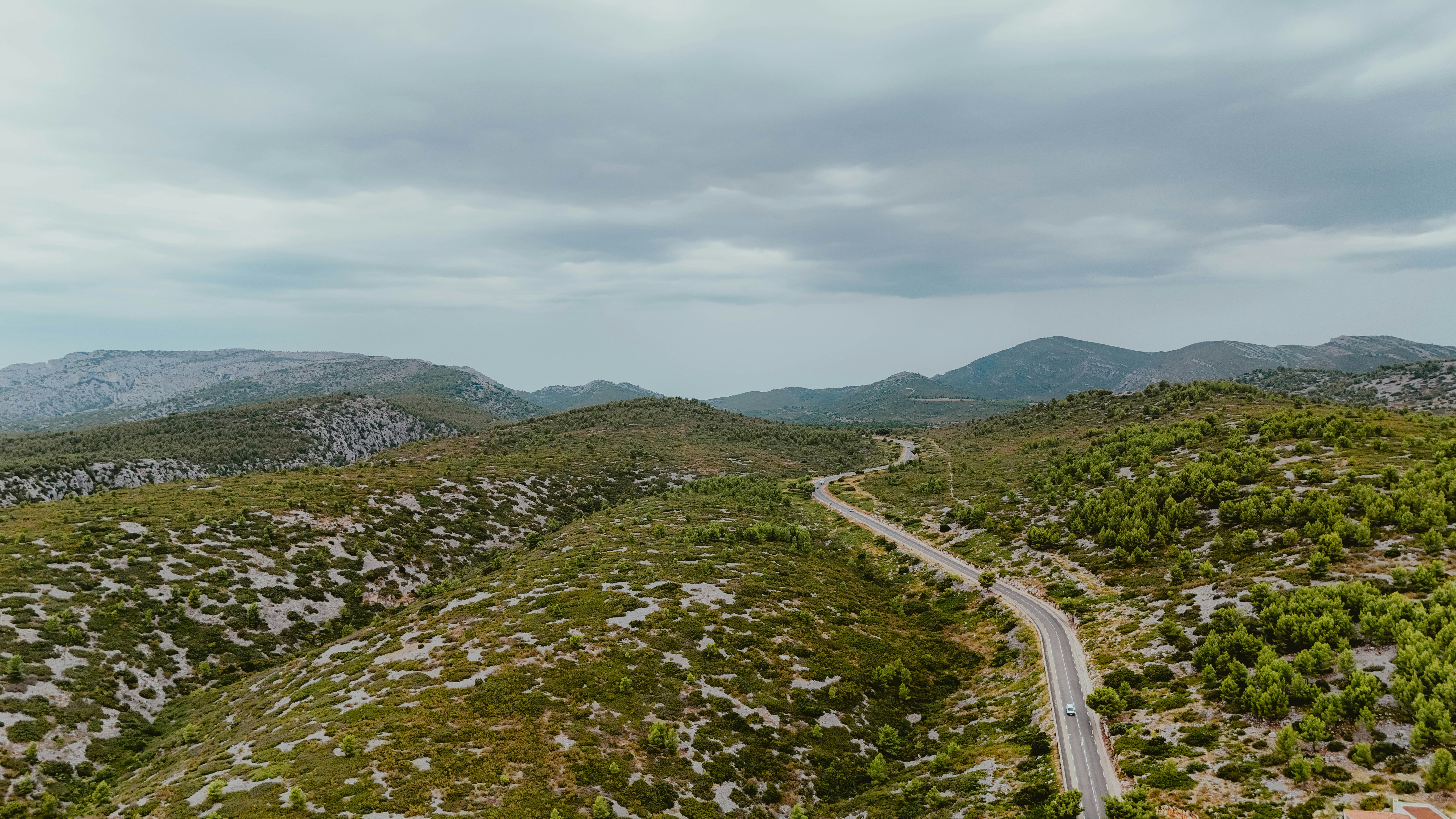 Winding road through green, rocky hills under cloudy sky
