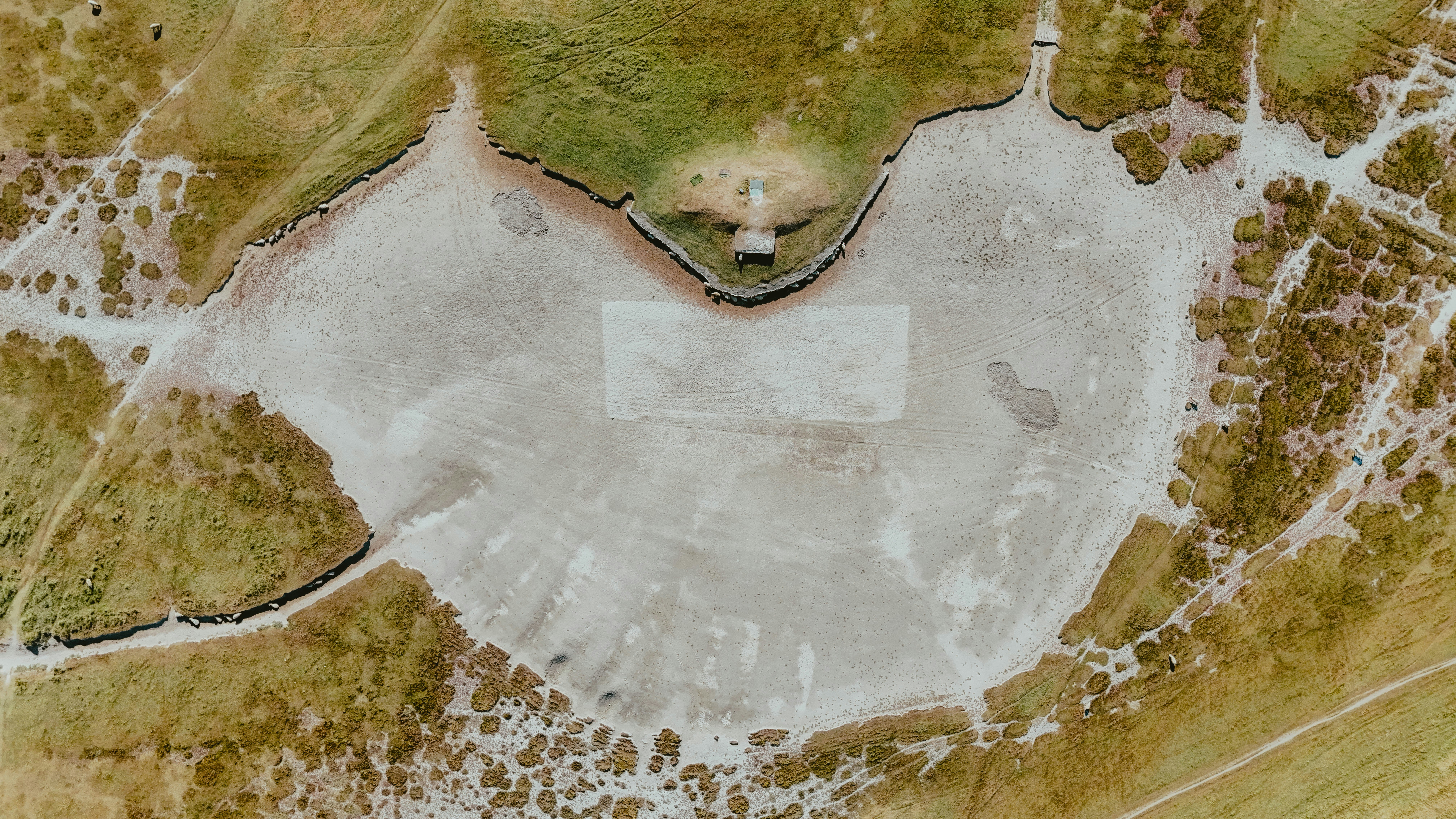 An aerial view showcasing a unique, eroded landscape with a distinct rectangular patch at the center, surrounded by grass and rocky textures.