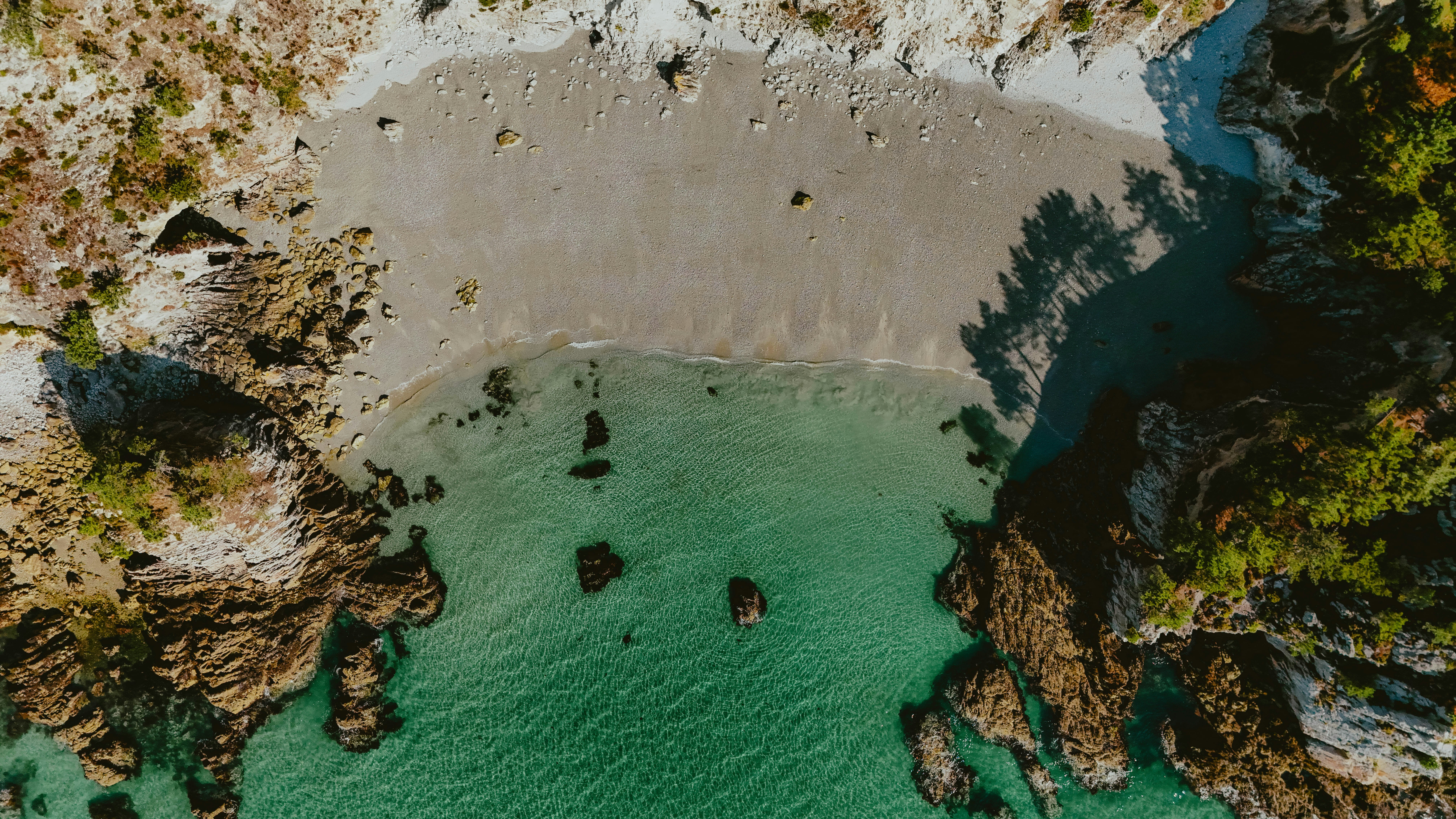 Aerial view of a secluded beach with turquoise waters and rocky formations, surrounded by lush greenery. The tranquil scene invites exploration.