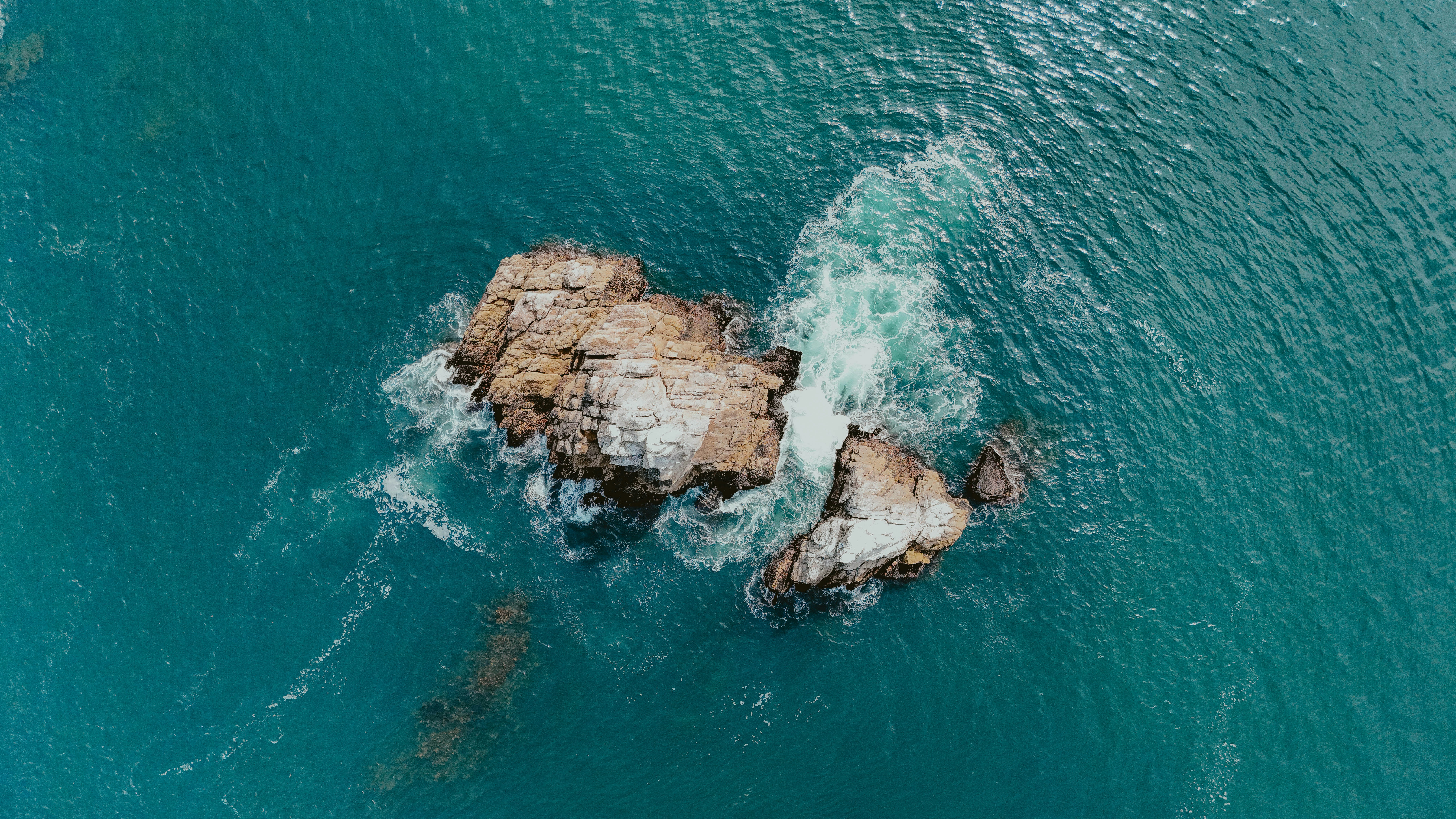 Rugged rock formation surrounded by vibrant turquoise waters, showcasing the dynamic interplay of ocean currents and rocky textures.