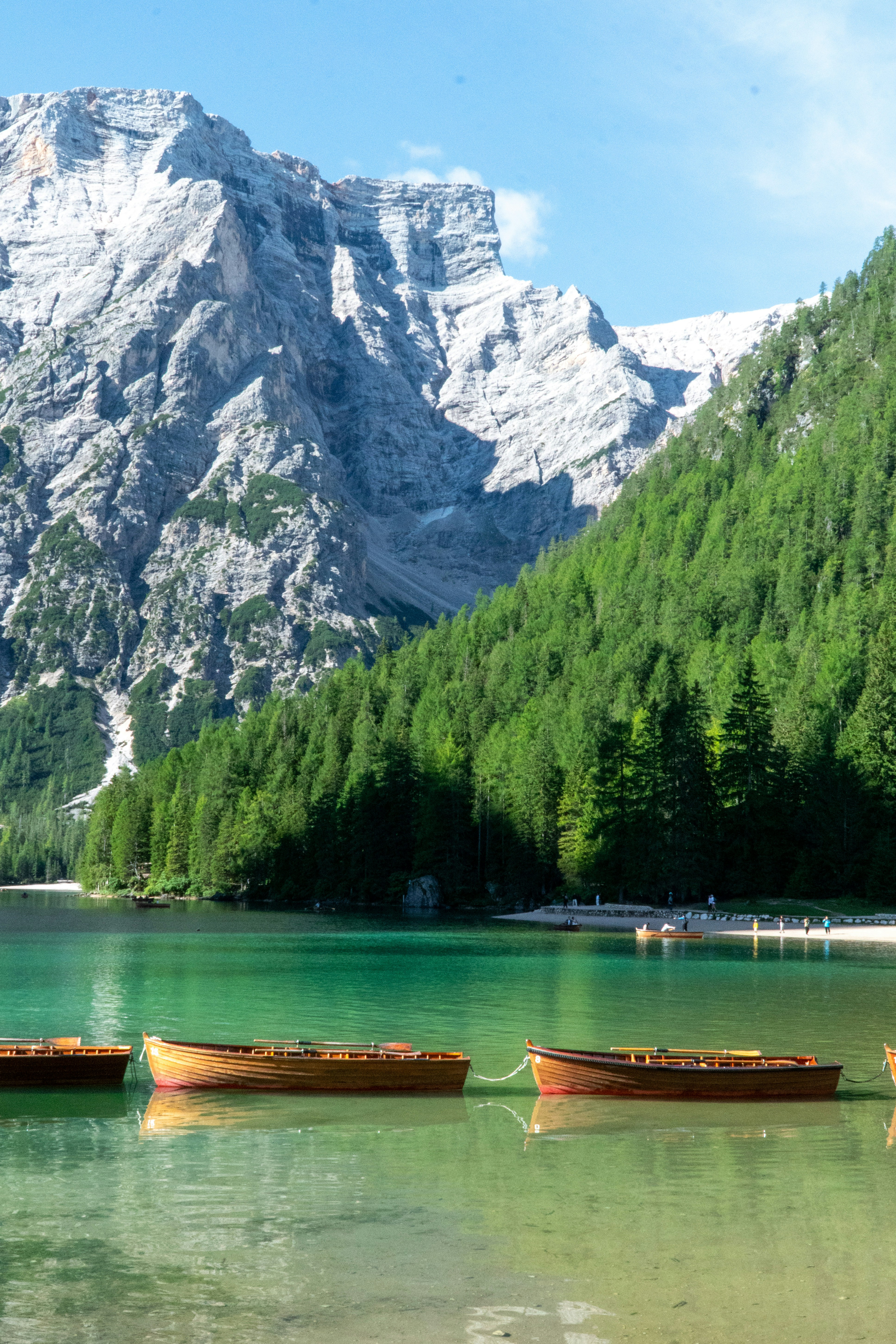 Wooden boats float on a clear turquoise lake with mountains.