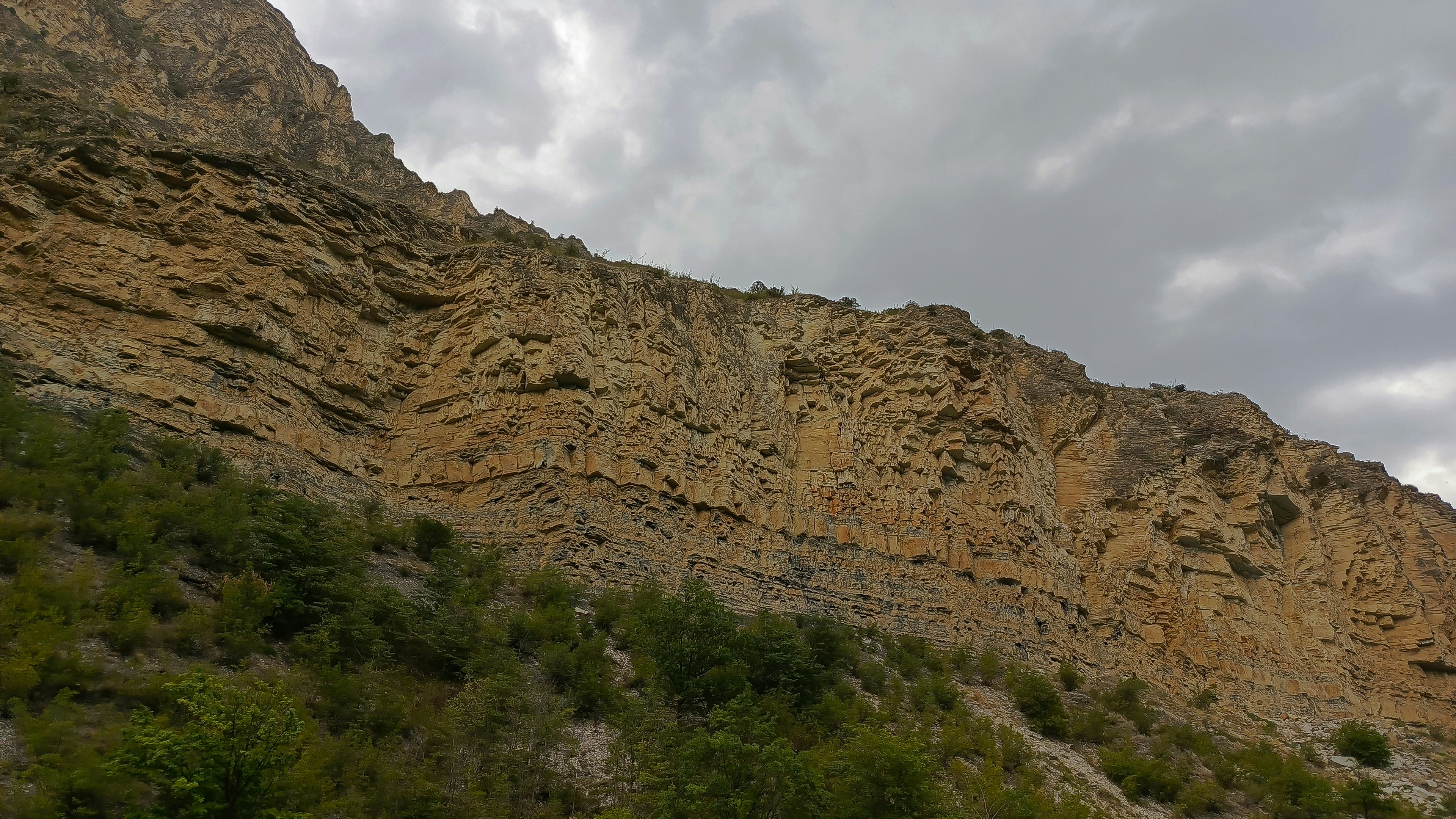 Rocky mountain slope with green vegetation under cloudy sky