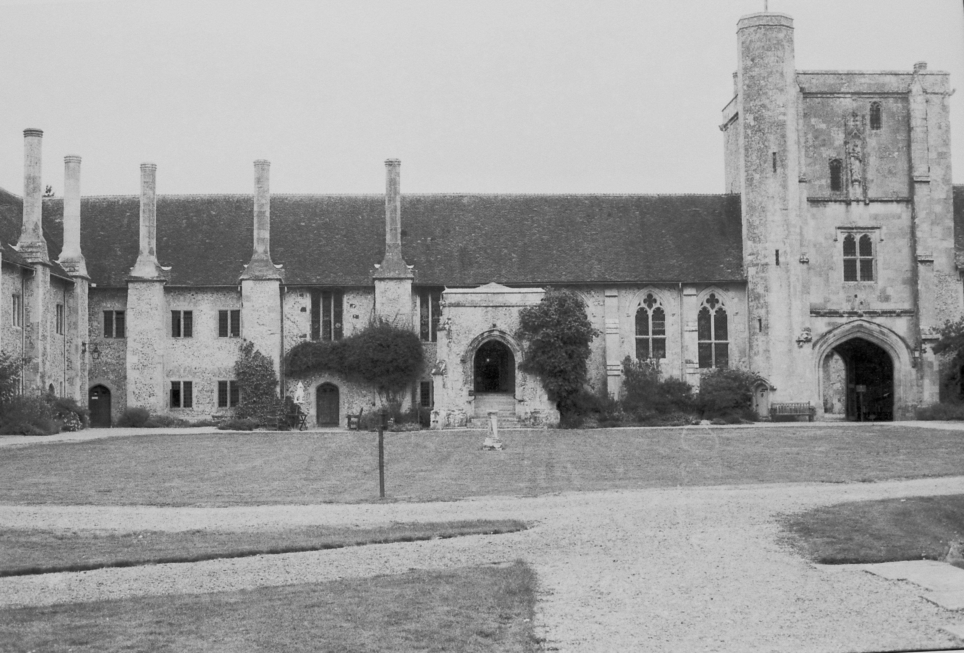 Historic stone building with tall chimneys and gothic architecture, framed by a manicured lawn and gravel path.