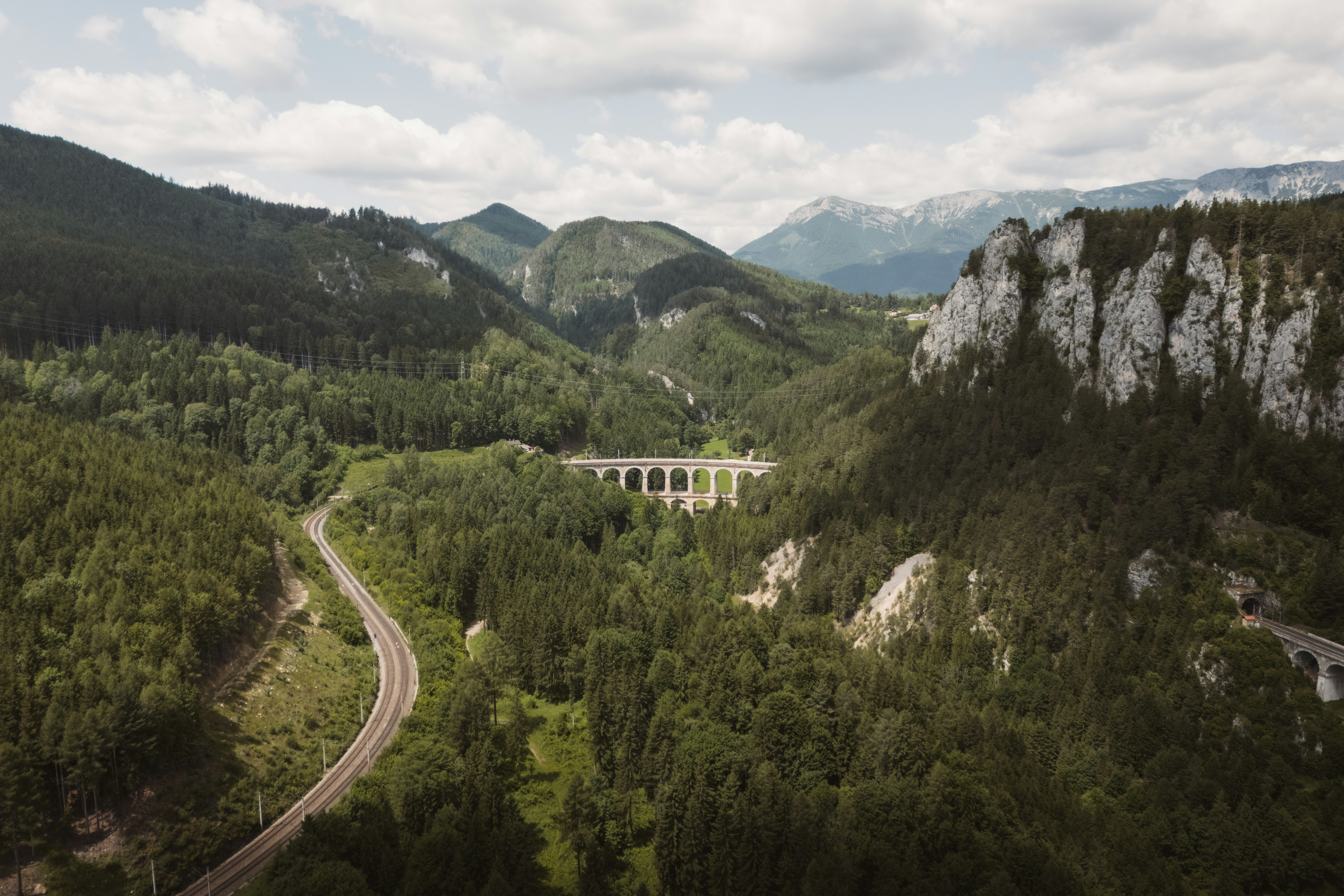 Majestic Viaduct in Mountain Valley | Train tracks curve through a lush green valley with mountains.