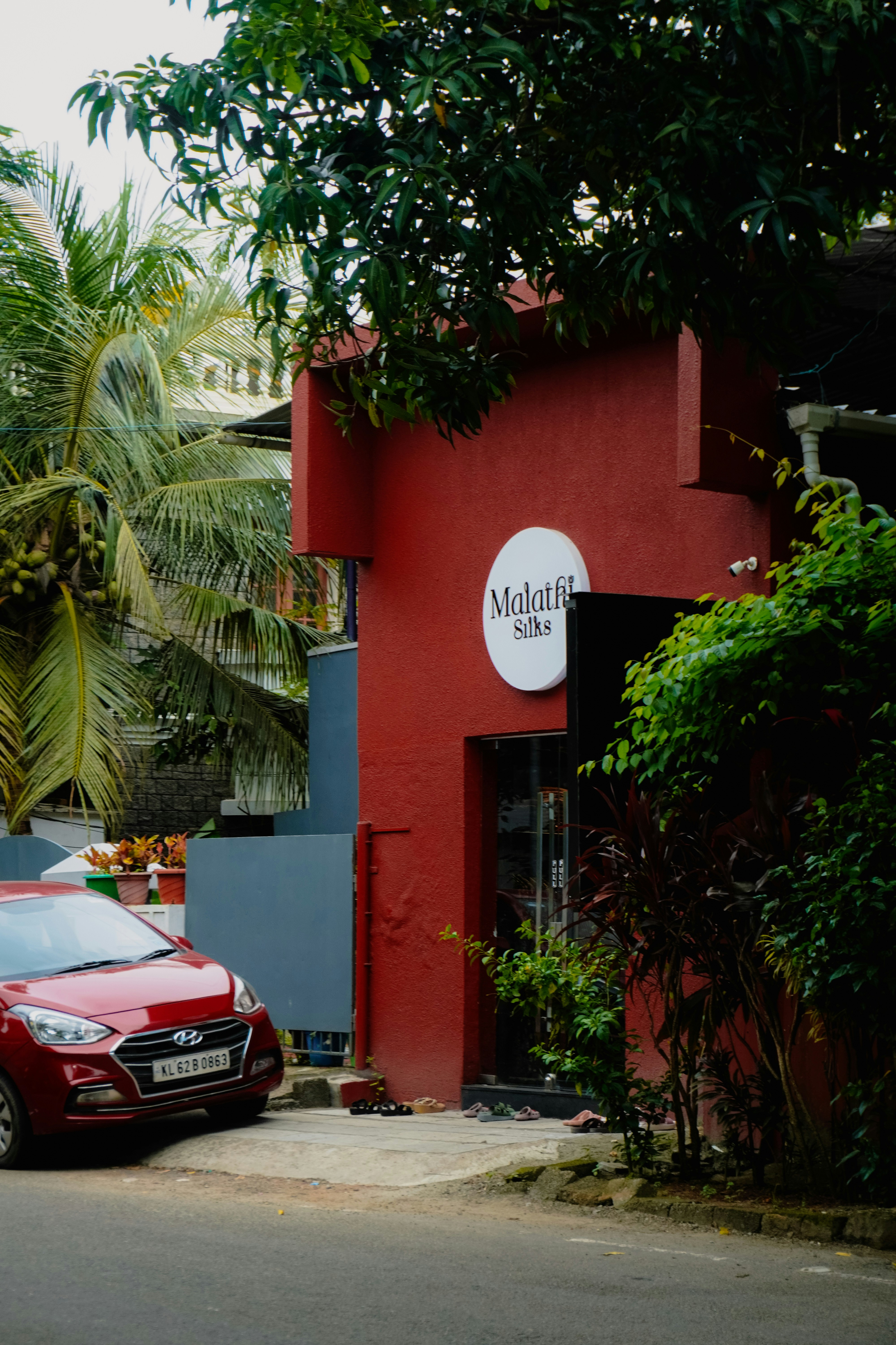 Red storefront and parked red car under tropical canopy