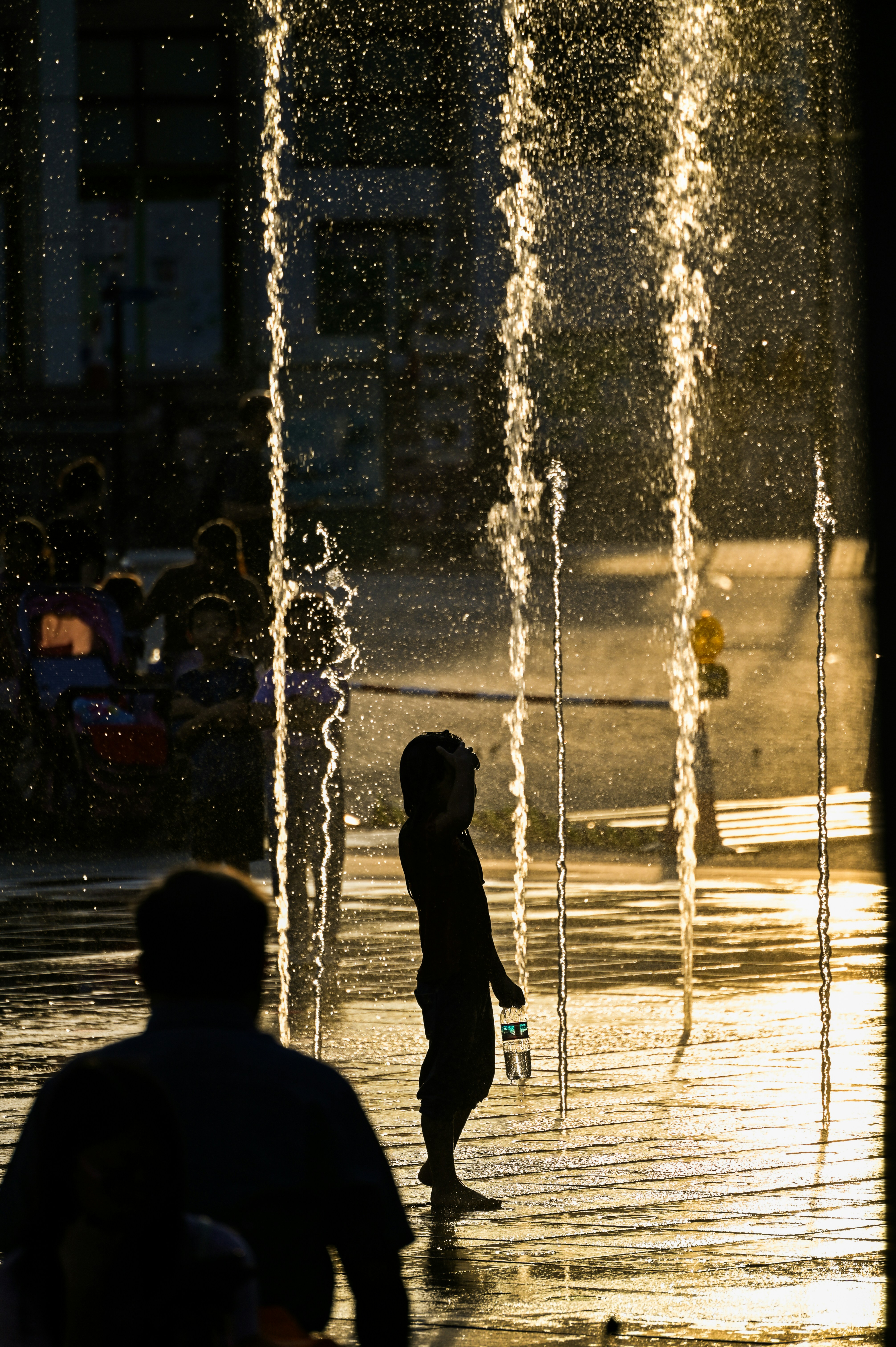 Silhouetted child plays in a water fountain at sunset.