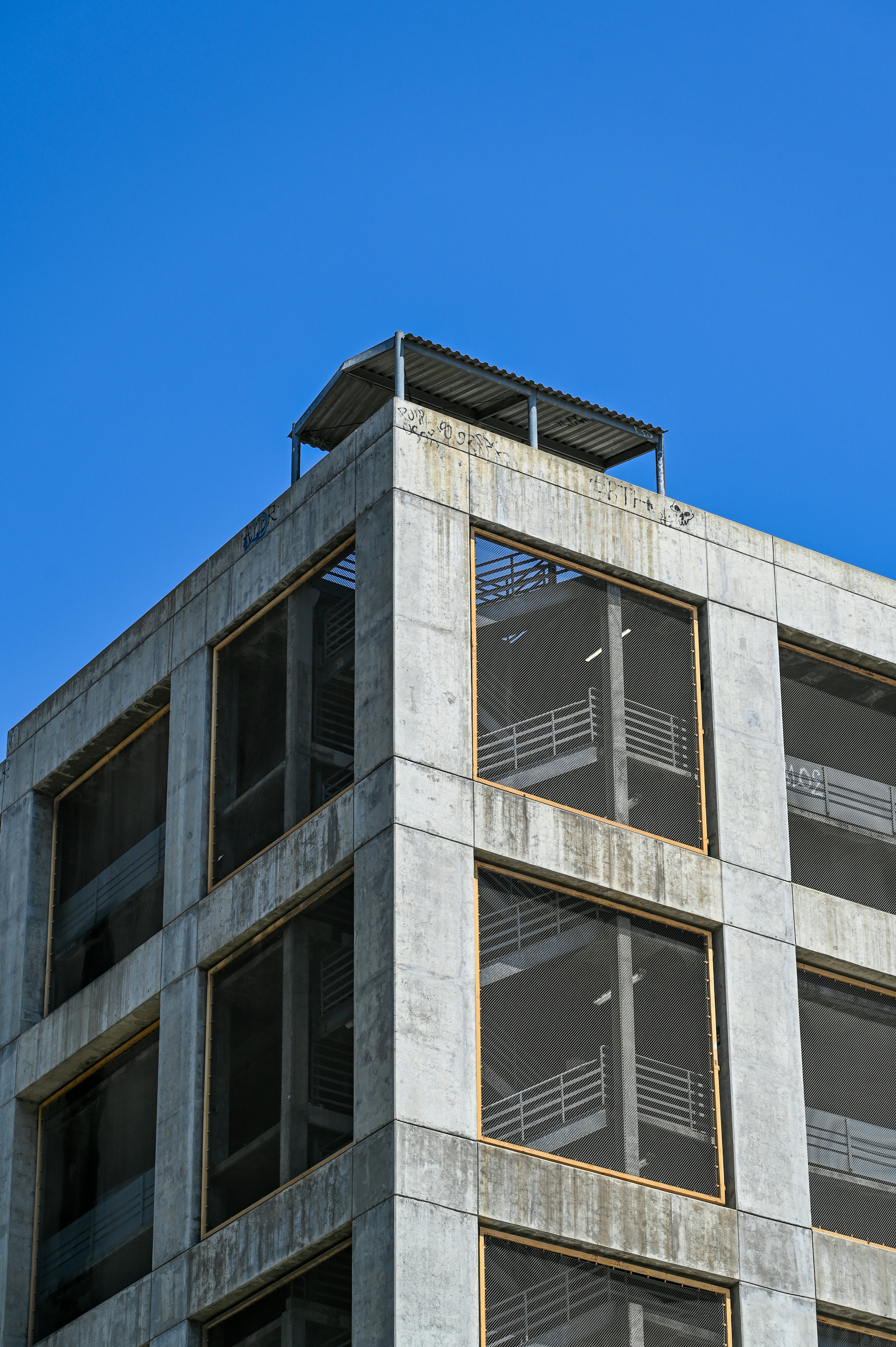 A modern concrete structure reaching towards the sky, showcasing its geometric lines and open spaces. The clear blue backdrop complements the industrial aesthetic.