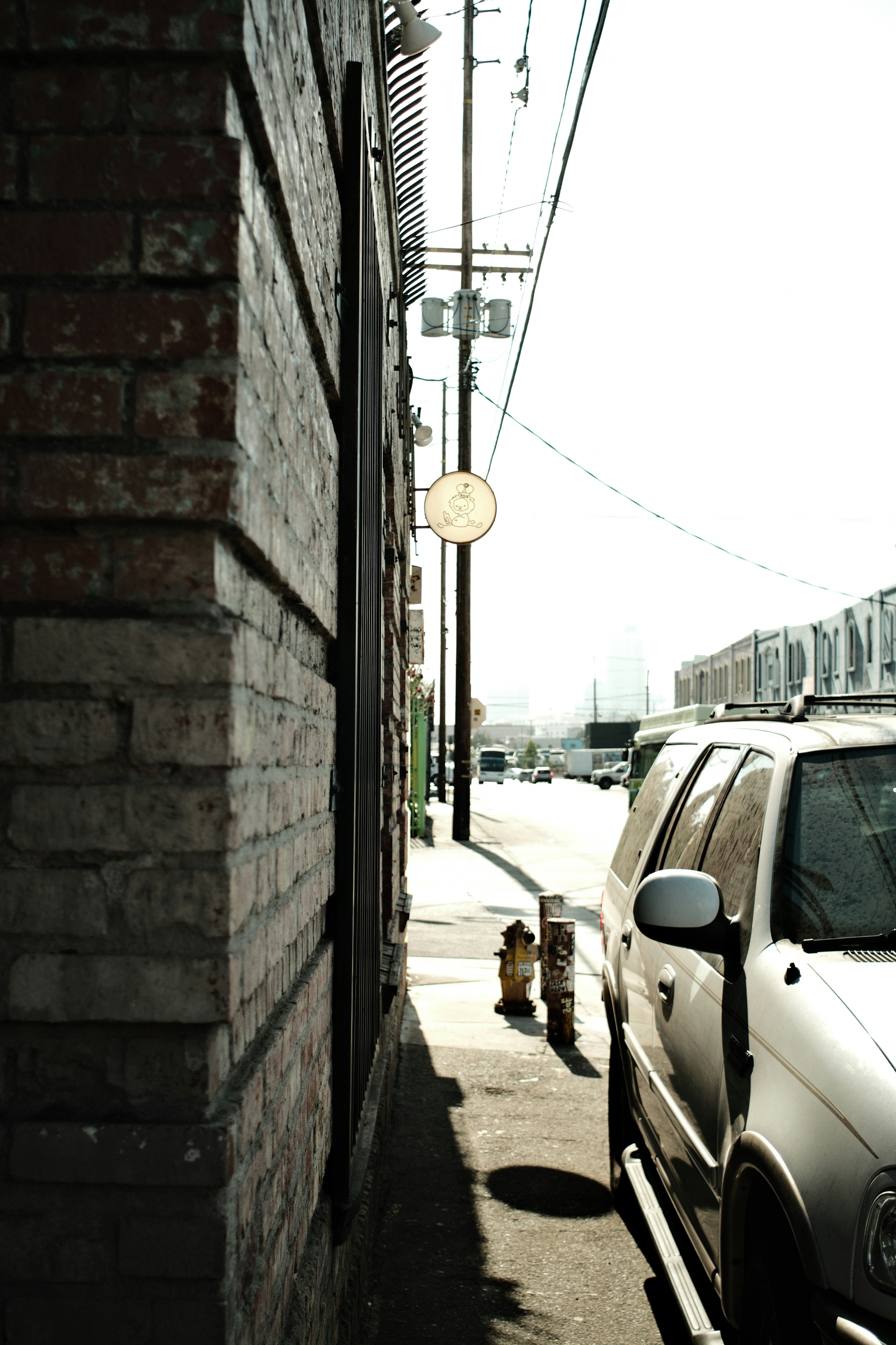 Sun-drenched street corner featuring a brick wall and a parked silver SUV, with a distant view of buildings. The scene captures the essence of urban life.