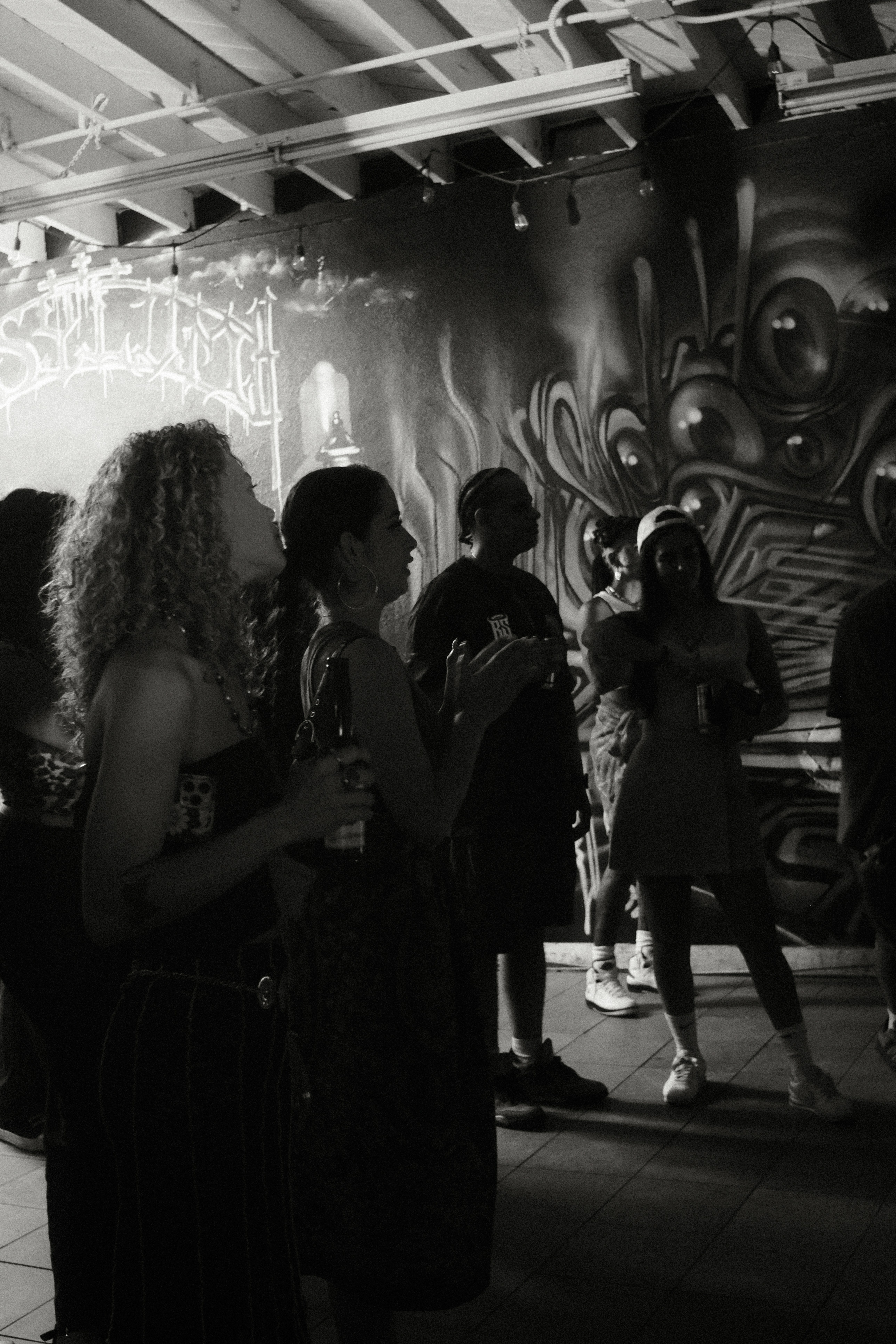 Group of individuals engaged in a lively moment within an artistic space, surrounded by vibrant graffiti. The atmosphere reflects a blend of culture and creativity.