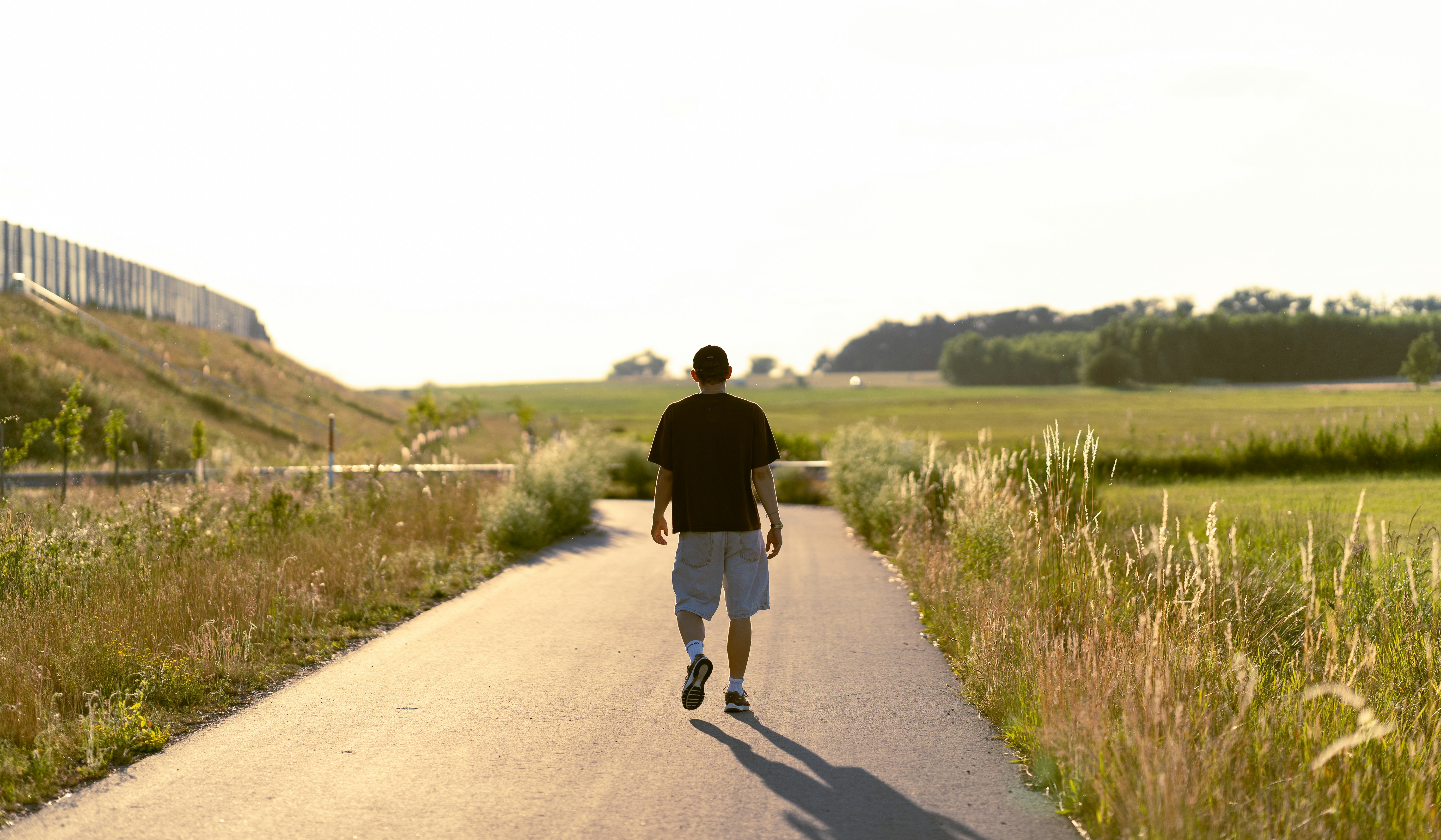Photo of a man walking on the road | Man walks down a path through fields.
