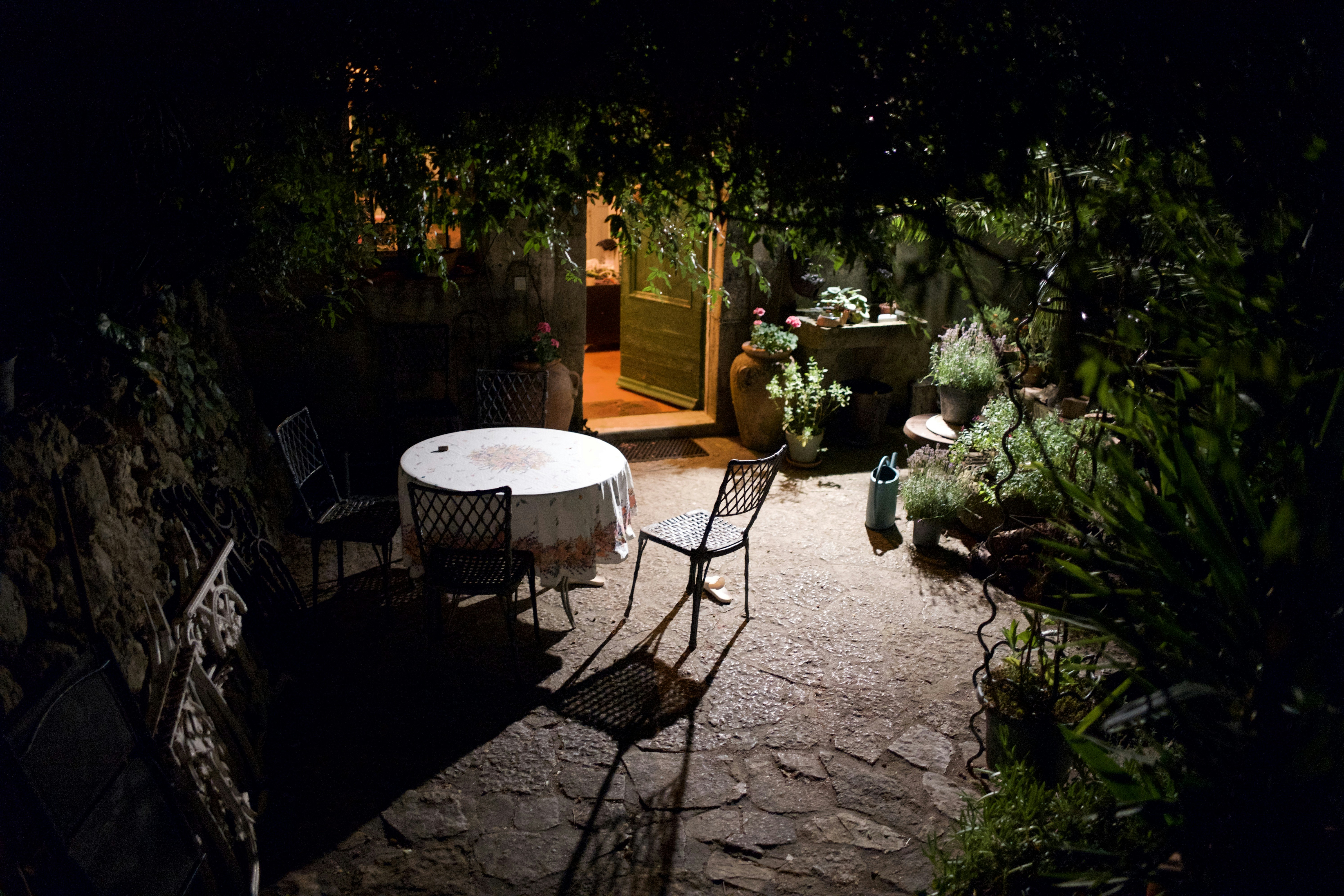 An inviting outdoor dining area illuminated by soft light, surrounded by lush greenery and rustic decor. A serene atmosphere invites relaxation and conversation.