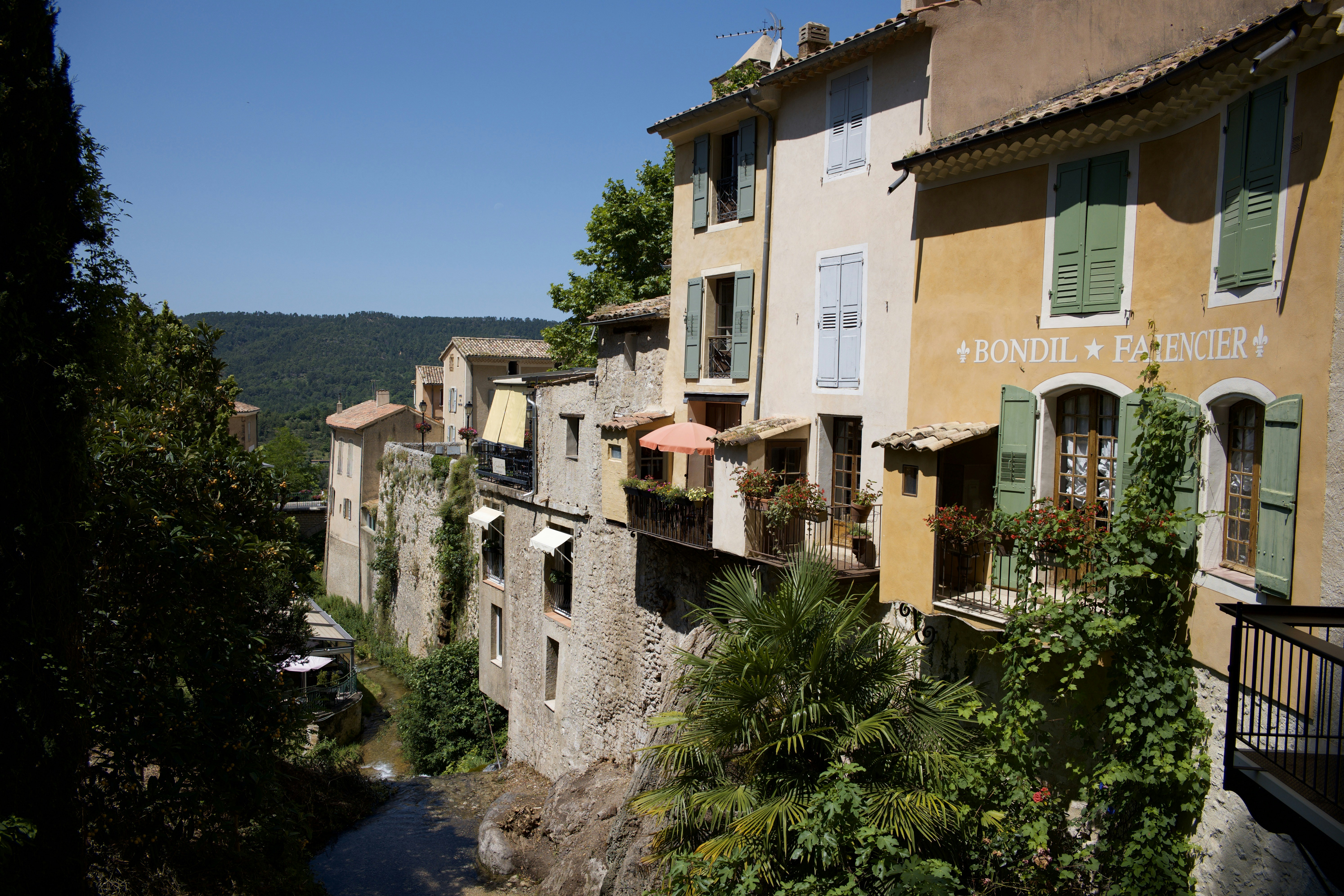 Terraced buildings with green shutters and balconies in sunlight.