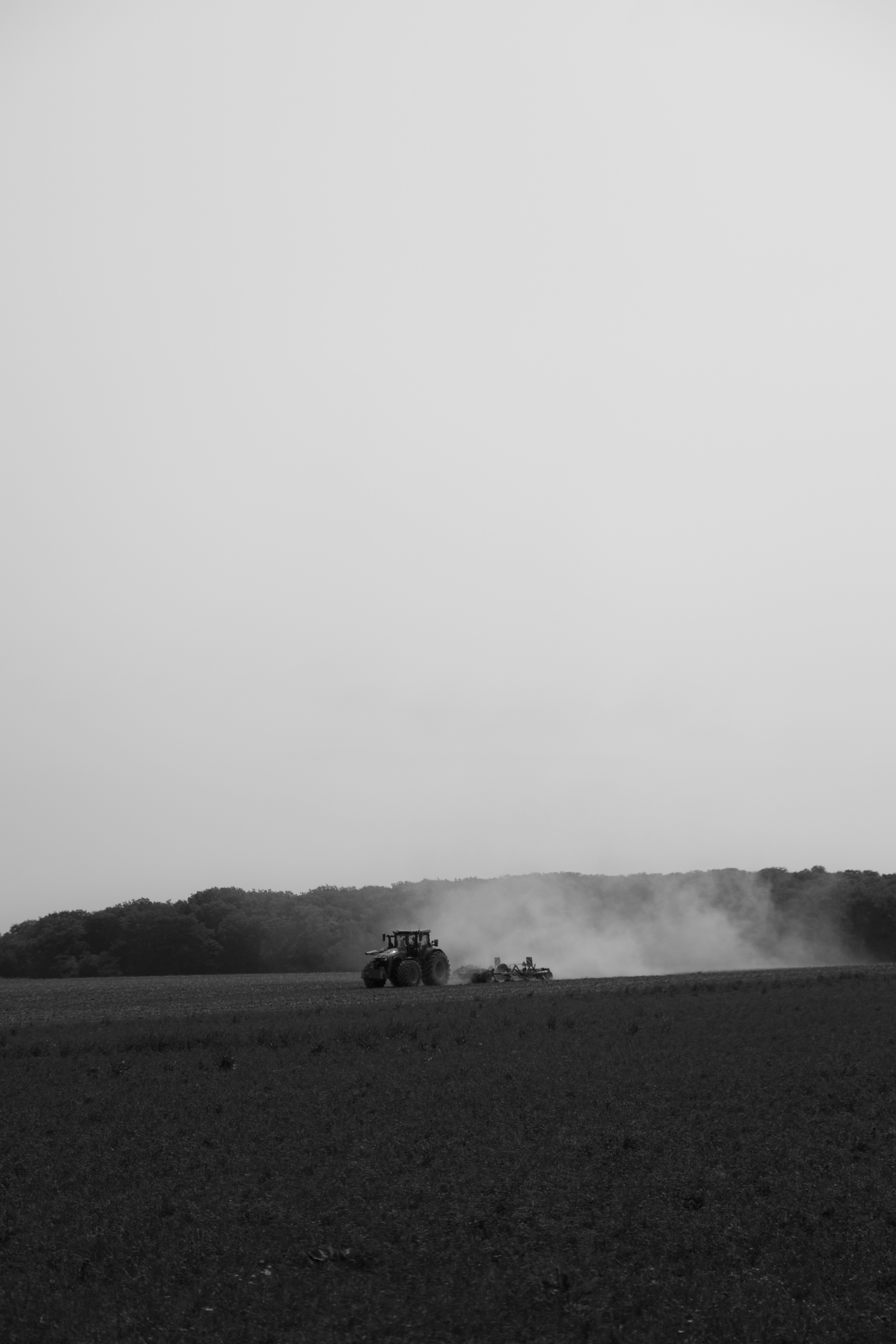 Tractor plowing a dusty field with trees behind