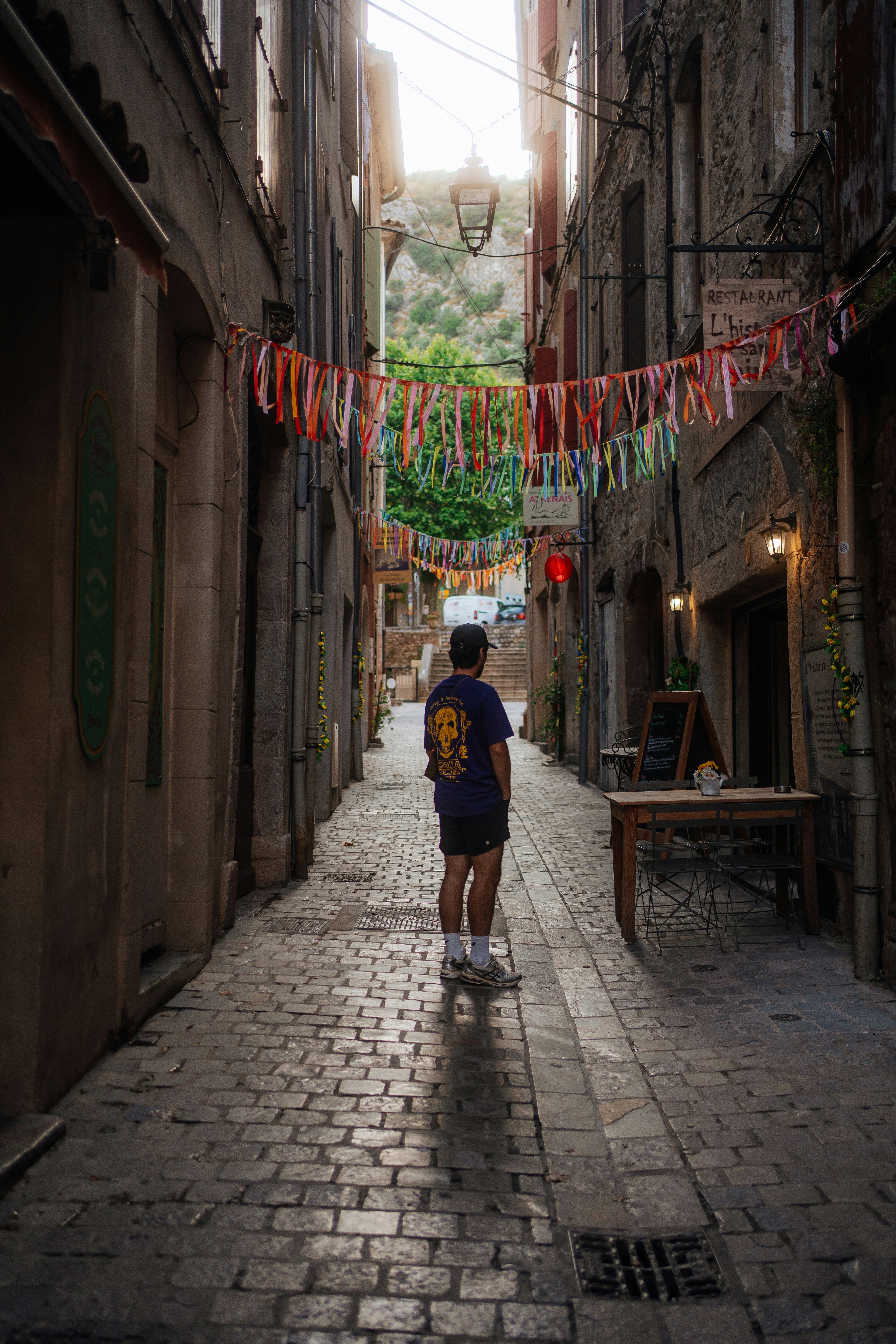 Man stands in a narrow european street with flags.