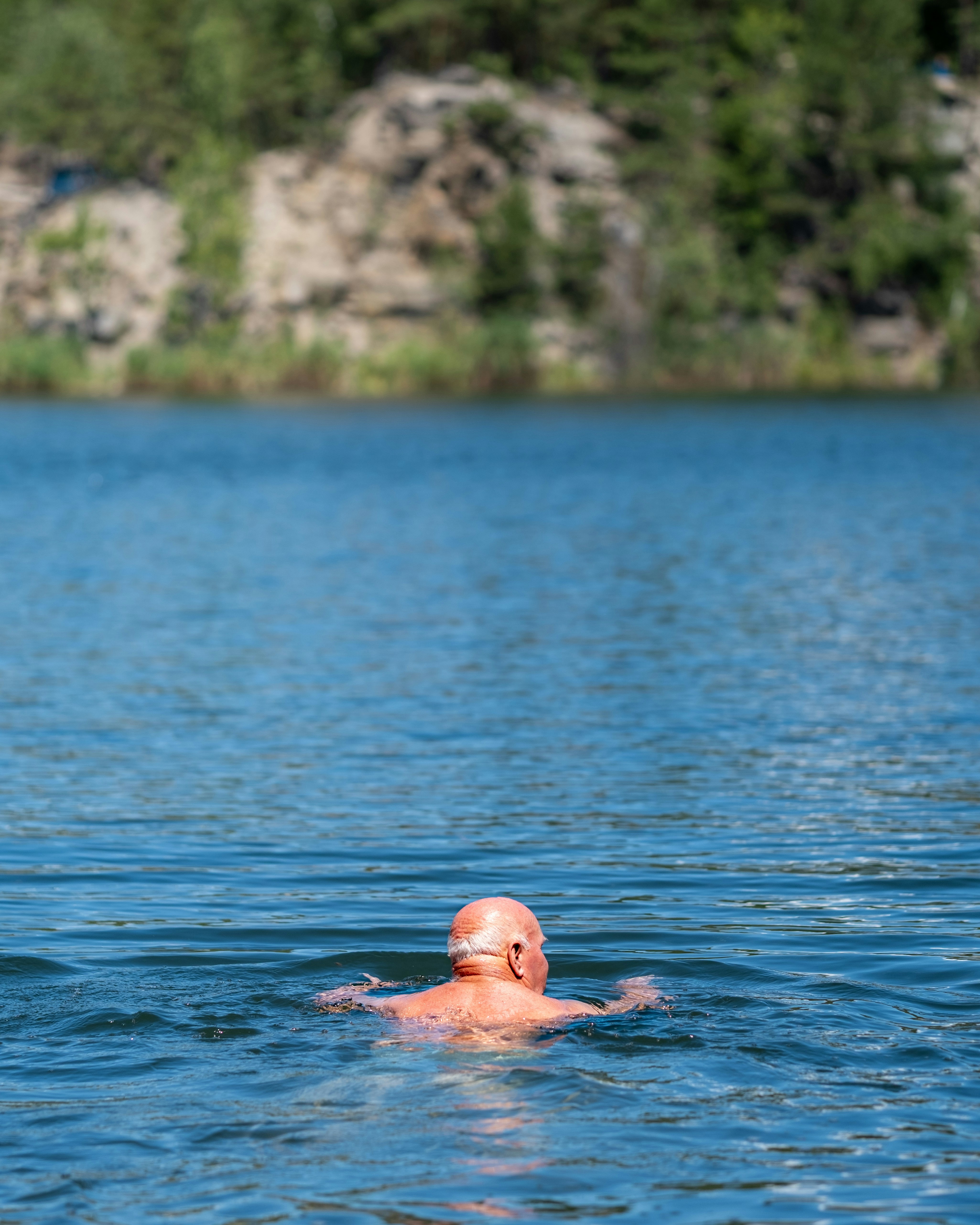 Man swimming in a blue lake with trees
