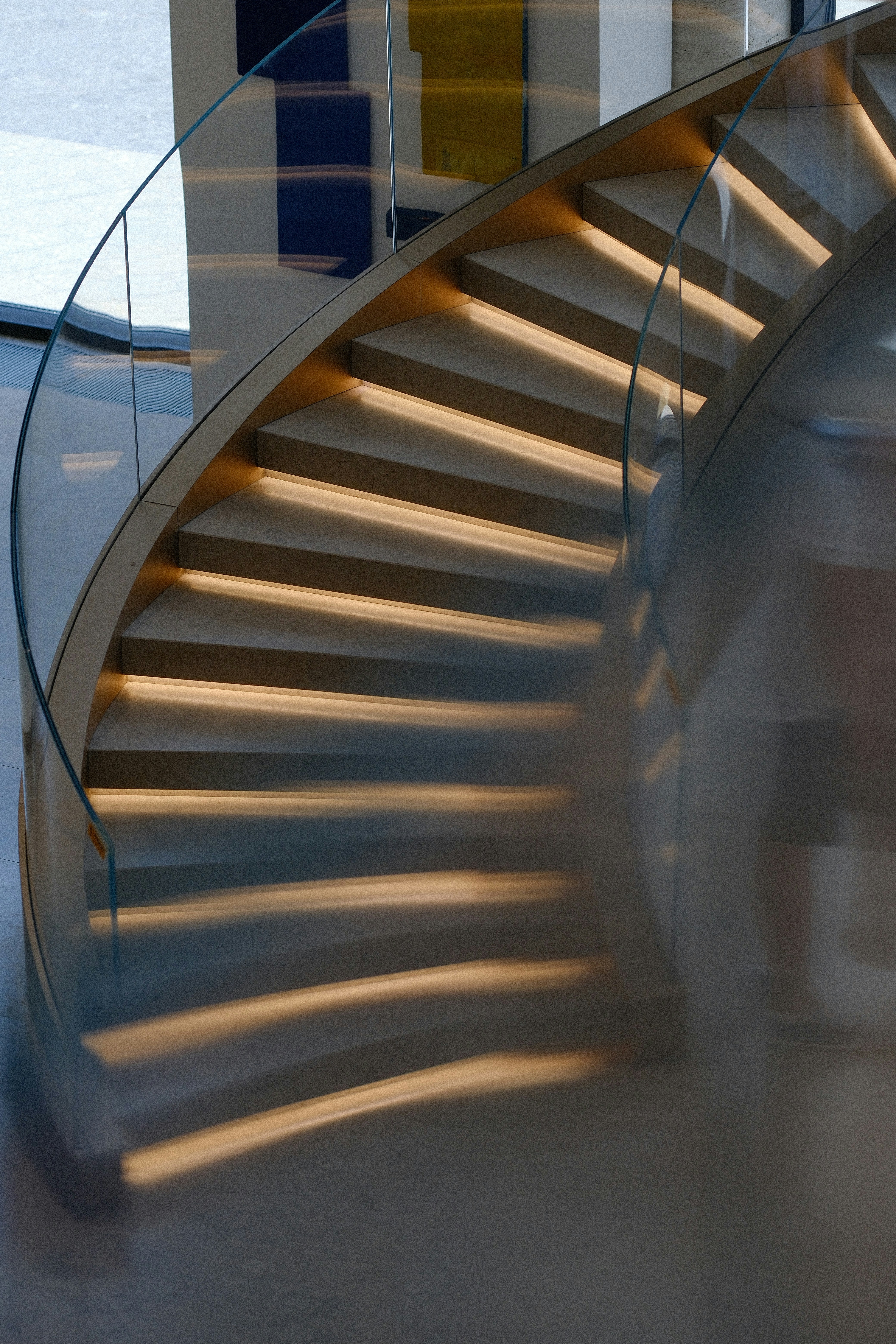Spiral staircase with softly illuminated steps, showcasing modern architectural design elements and a sleek glass railing.