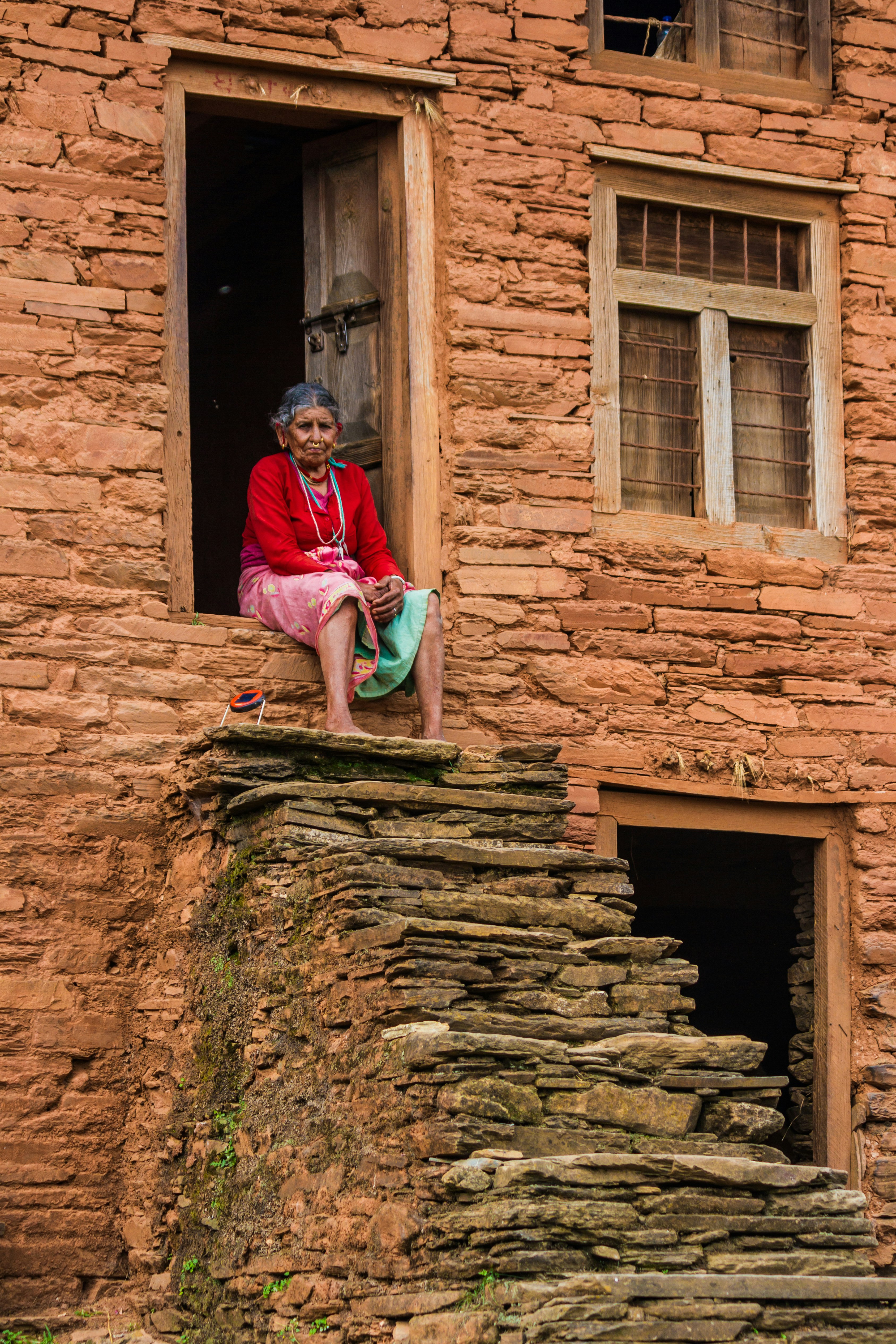 Elderly Woman in Doorway | Elderly woman sits on stone steps outside brick house.