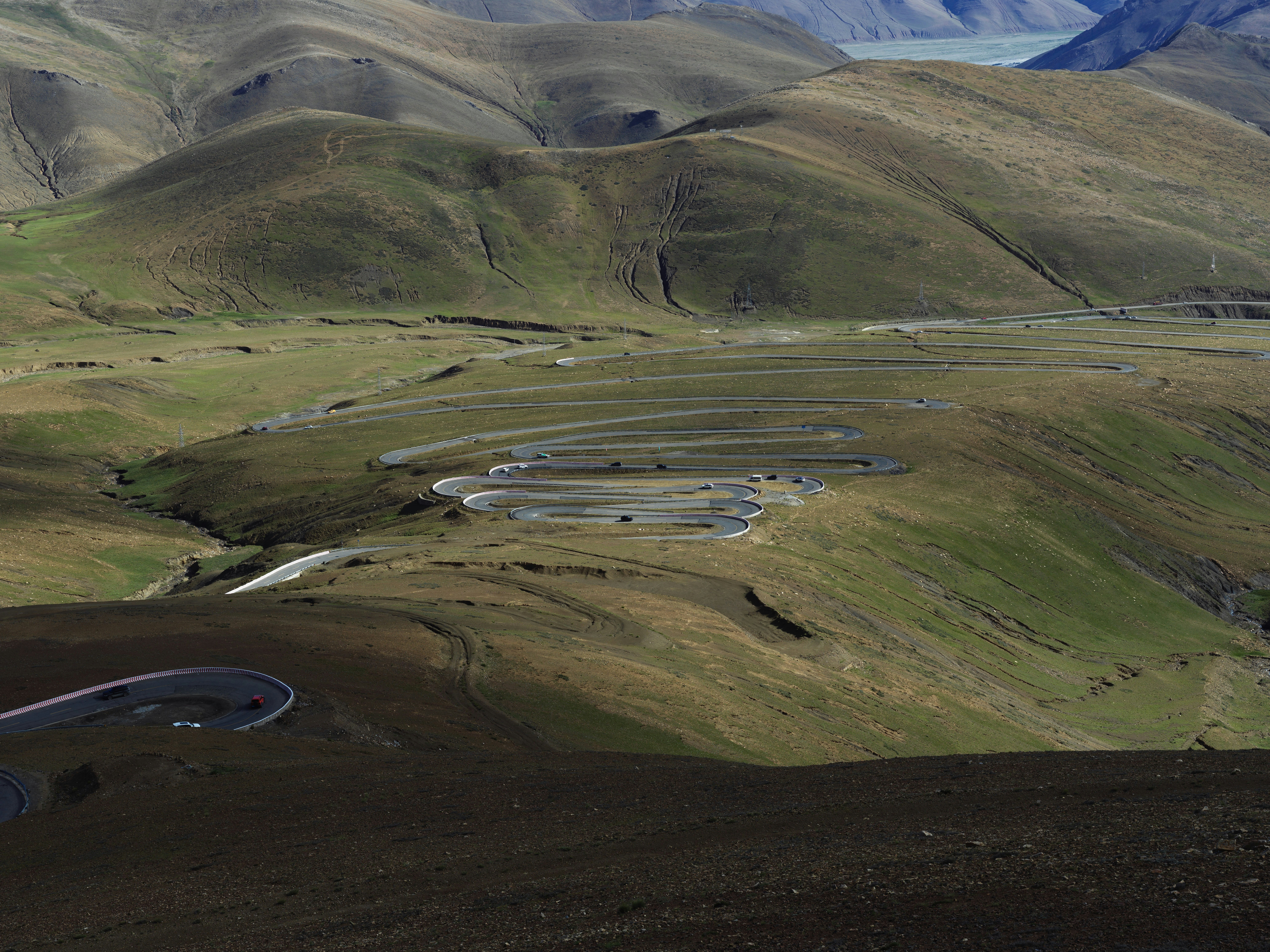 Winding road snakes through grassy hills, showcasing a dramatic landscape with sharp curves and elevation changes.