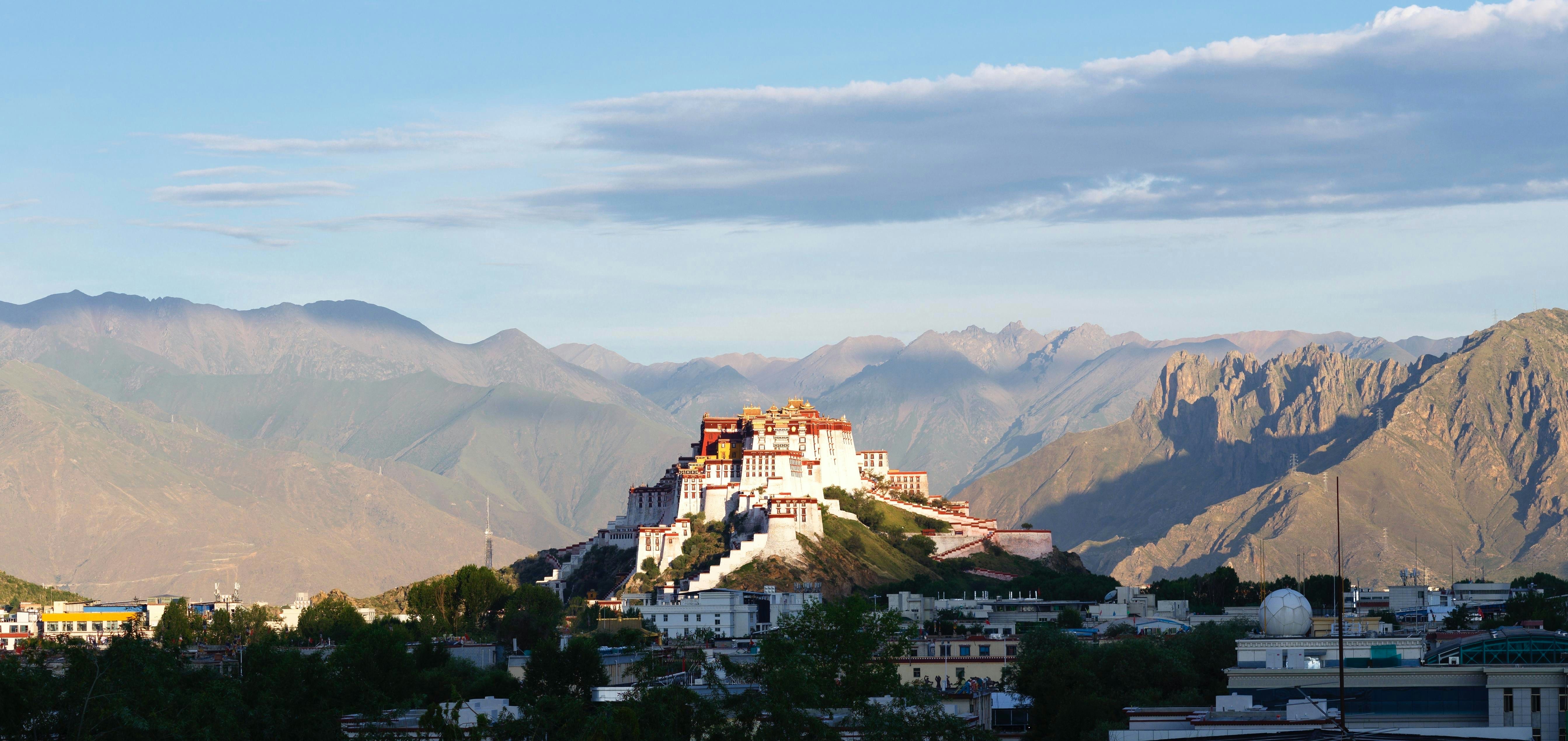 The sun rising over the Potala Palace. | Potala palace perched on a hill with mountains behind.