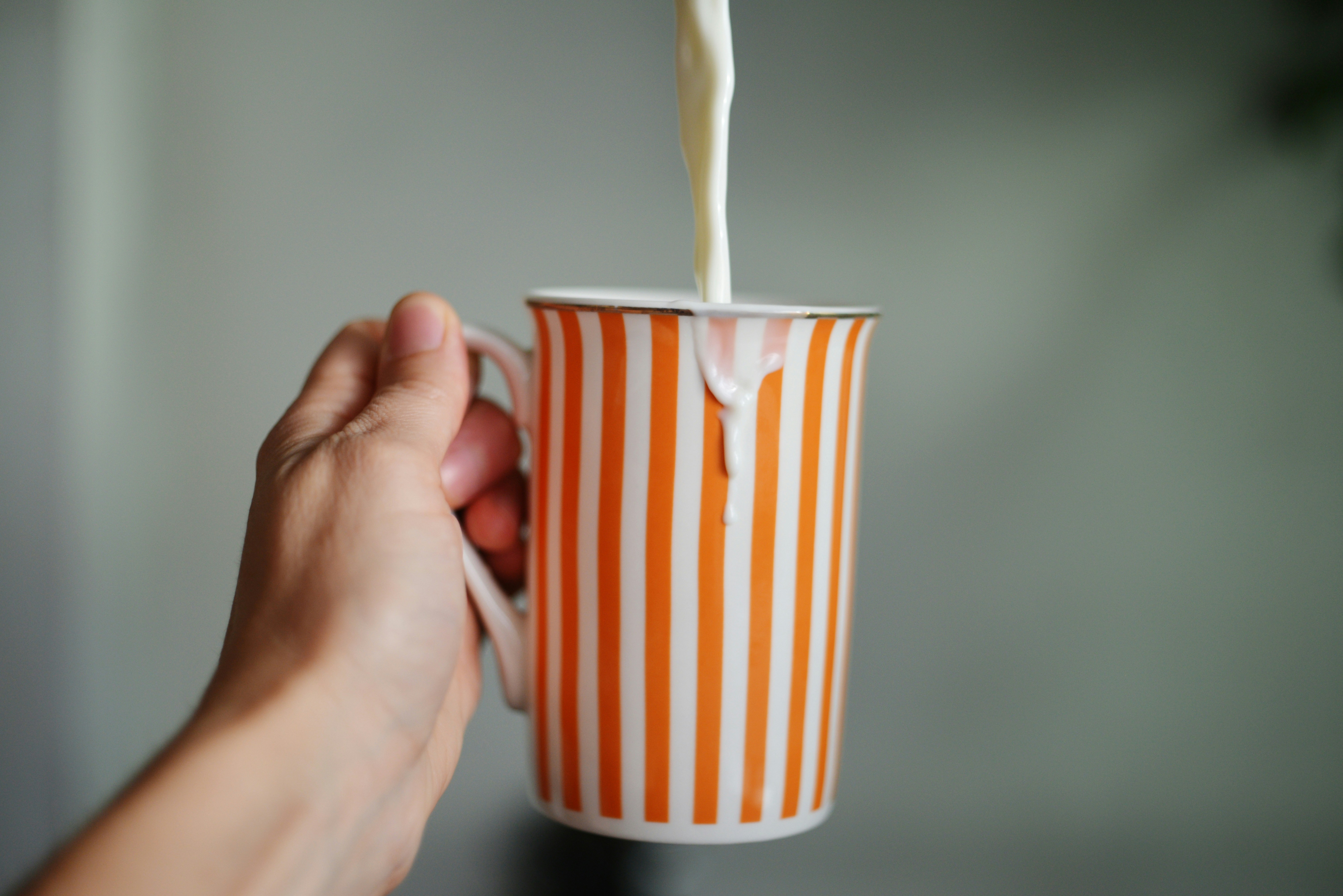 Milk being poured into a striped mug.