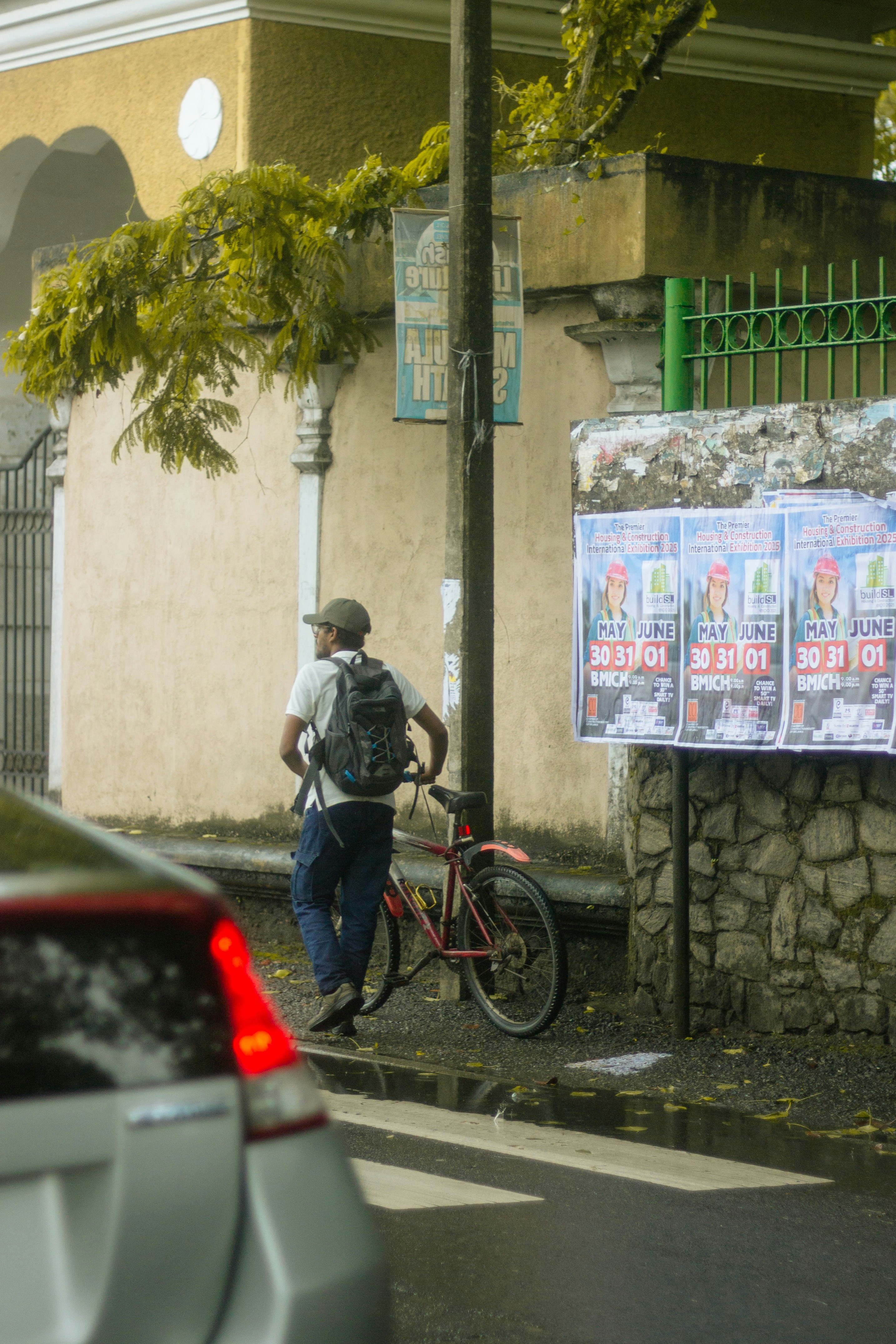 Man with backpack and bicycle leans on pole.