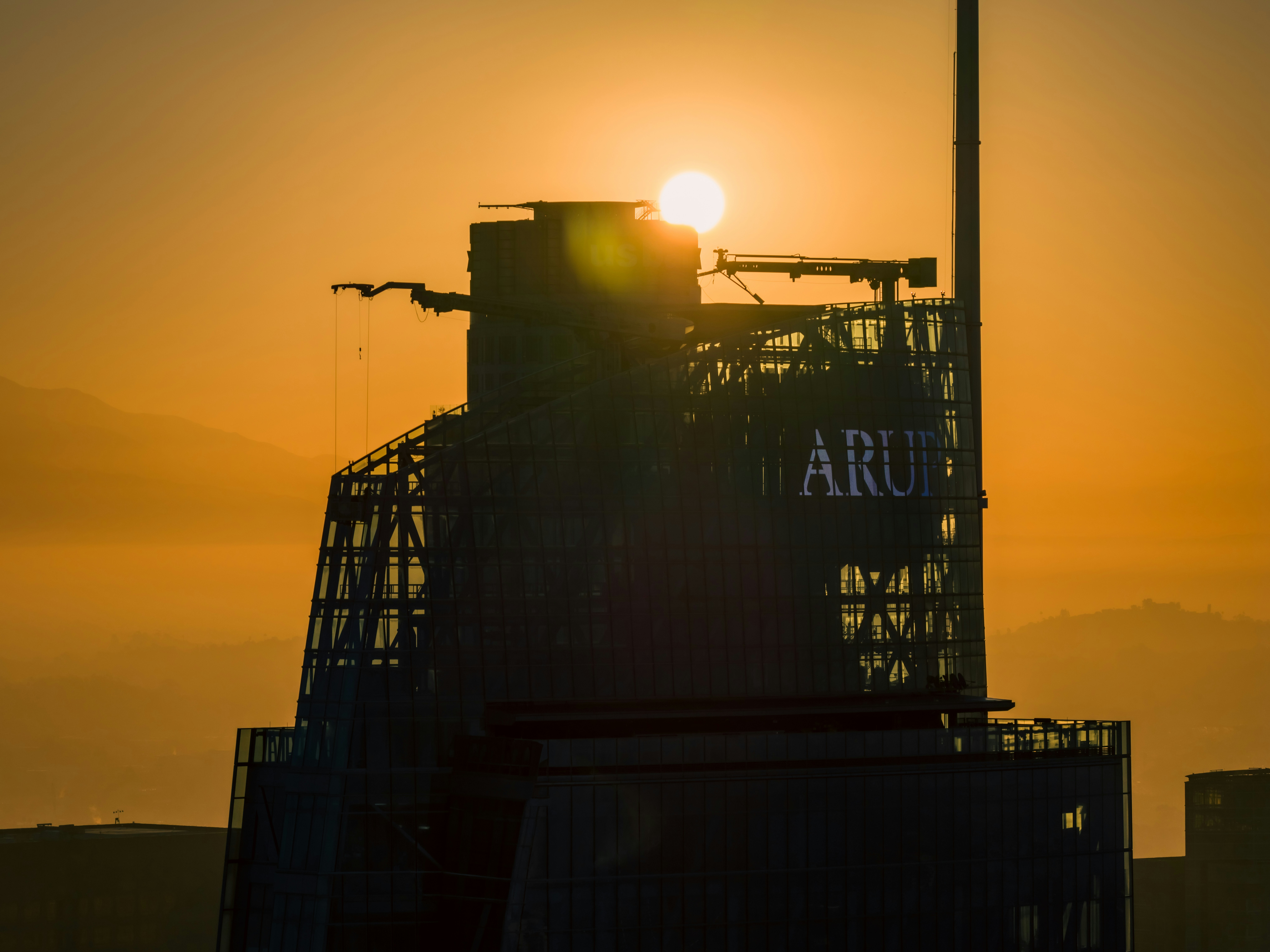 Sun setting behind a silhouetted building under construction.