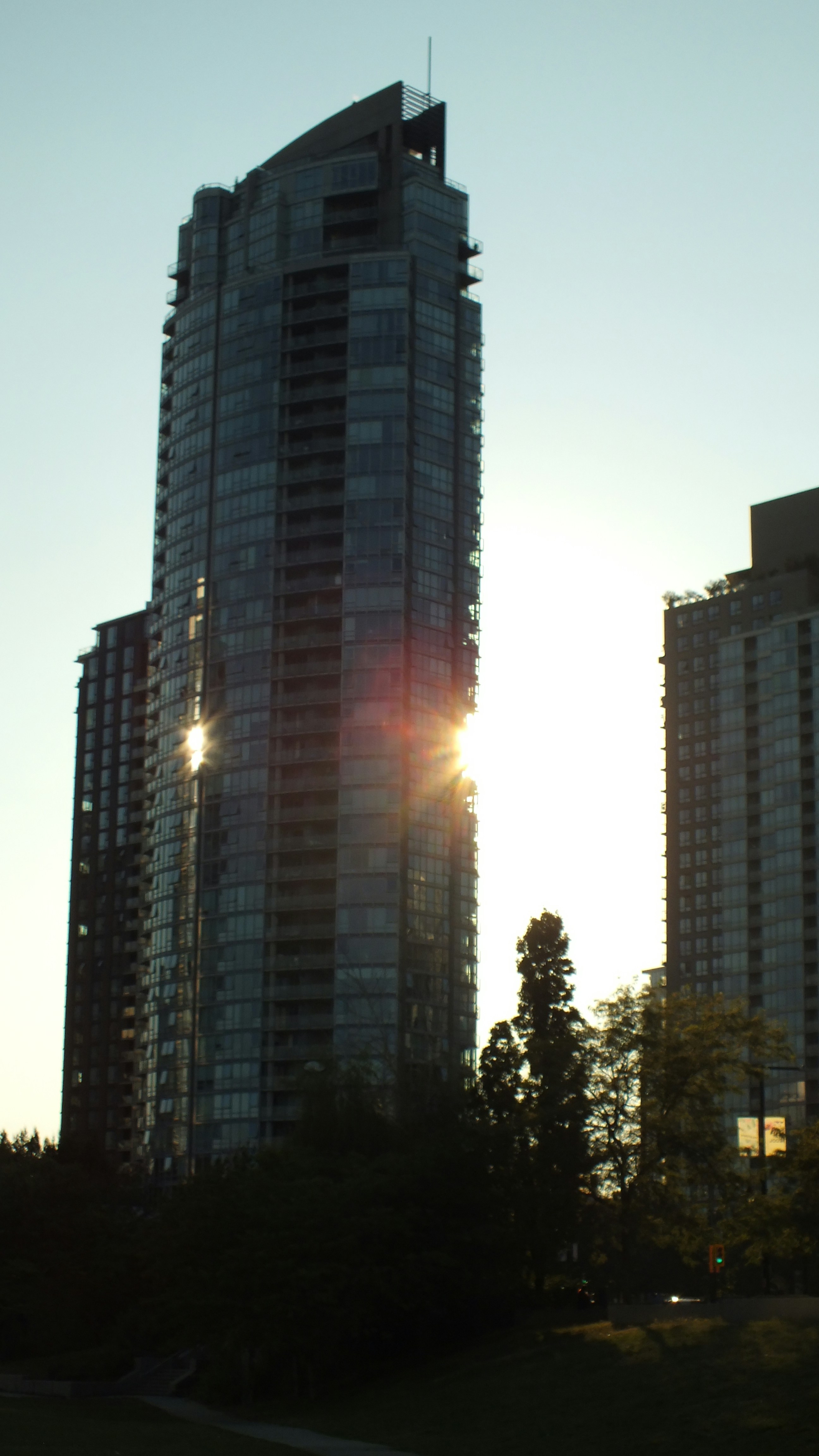 Silhouetted skyscrapers reflecting sunlight in a cityscape during sunset. The interplay of light creates a striking visual contrast.