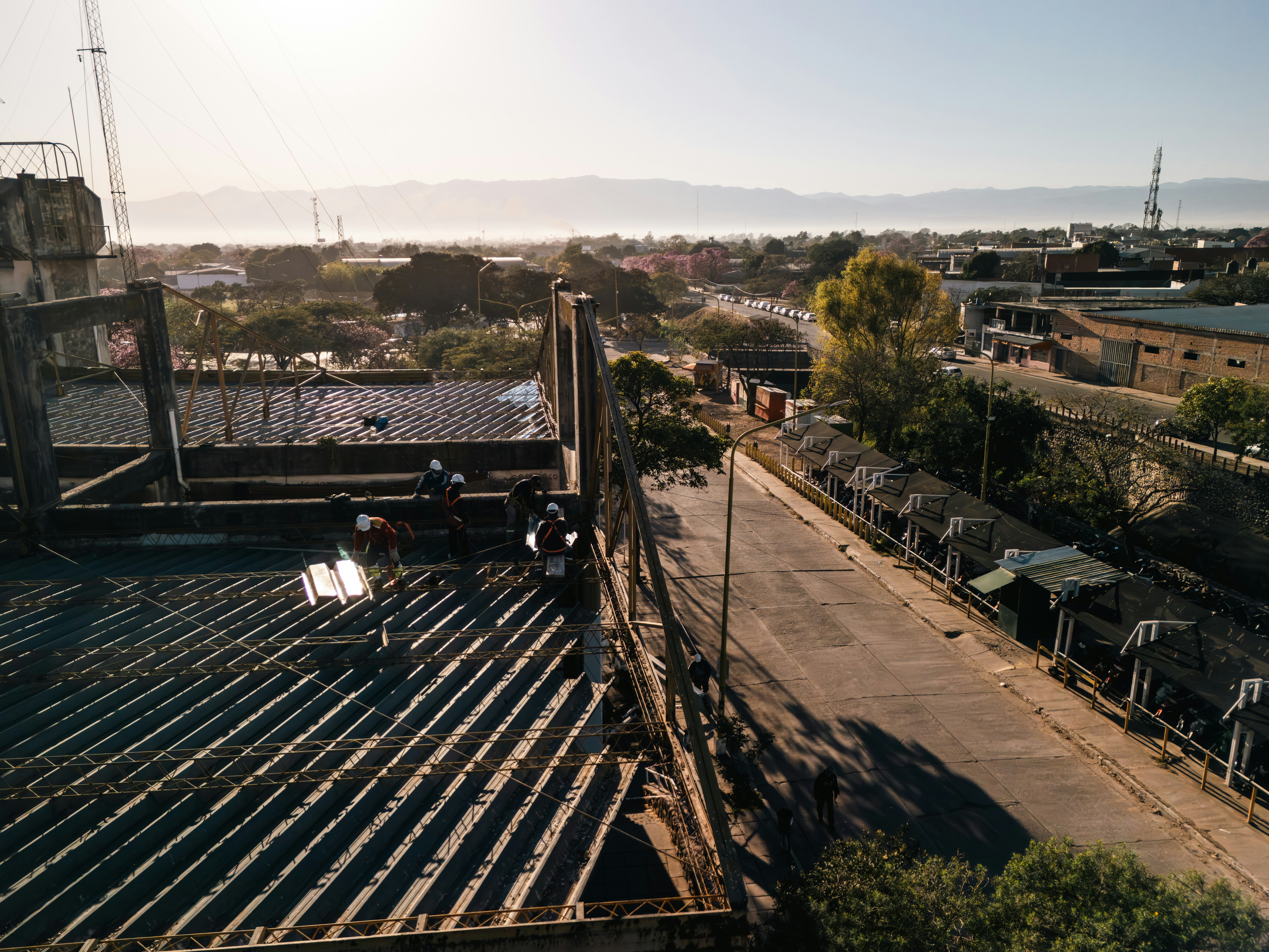 Terminal de Omnibus - Ciudad de San Pedro de Jujuy - Jujuy - Argentina | Workers on a rooftop near a bridge at sunset.