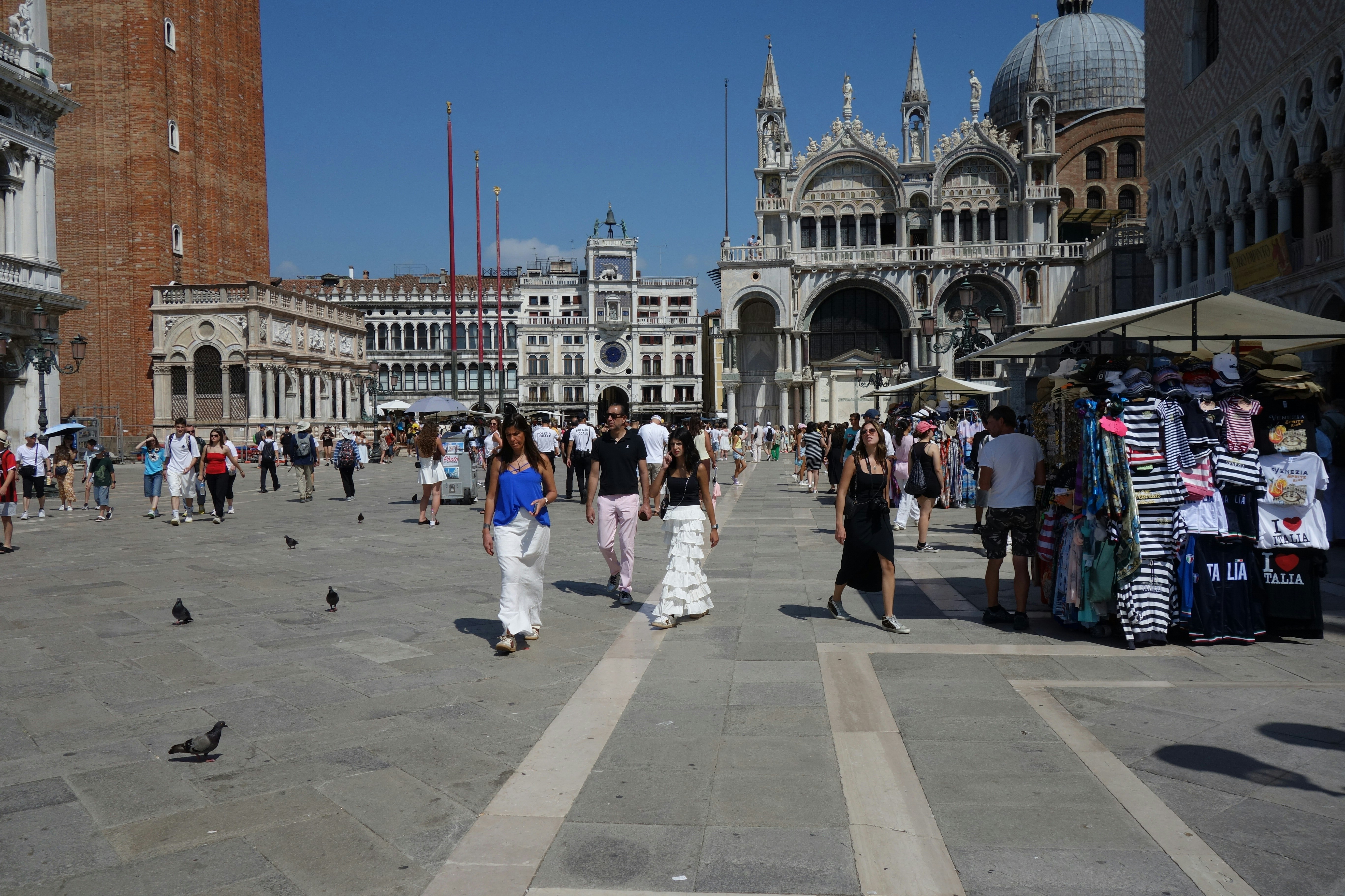 Tourists stroll through a sunny european plaza with architecture.