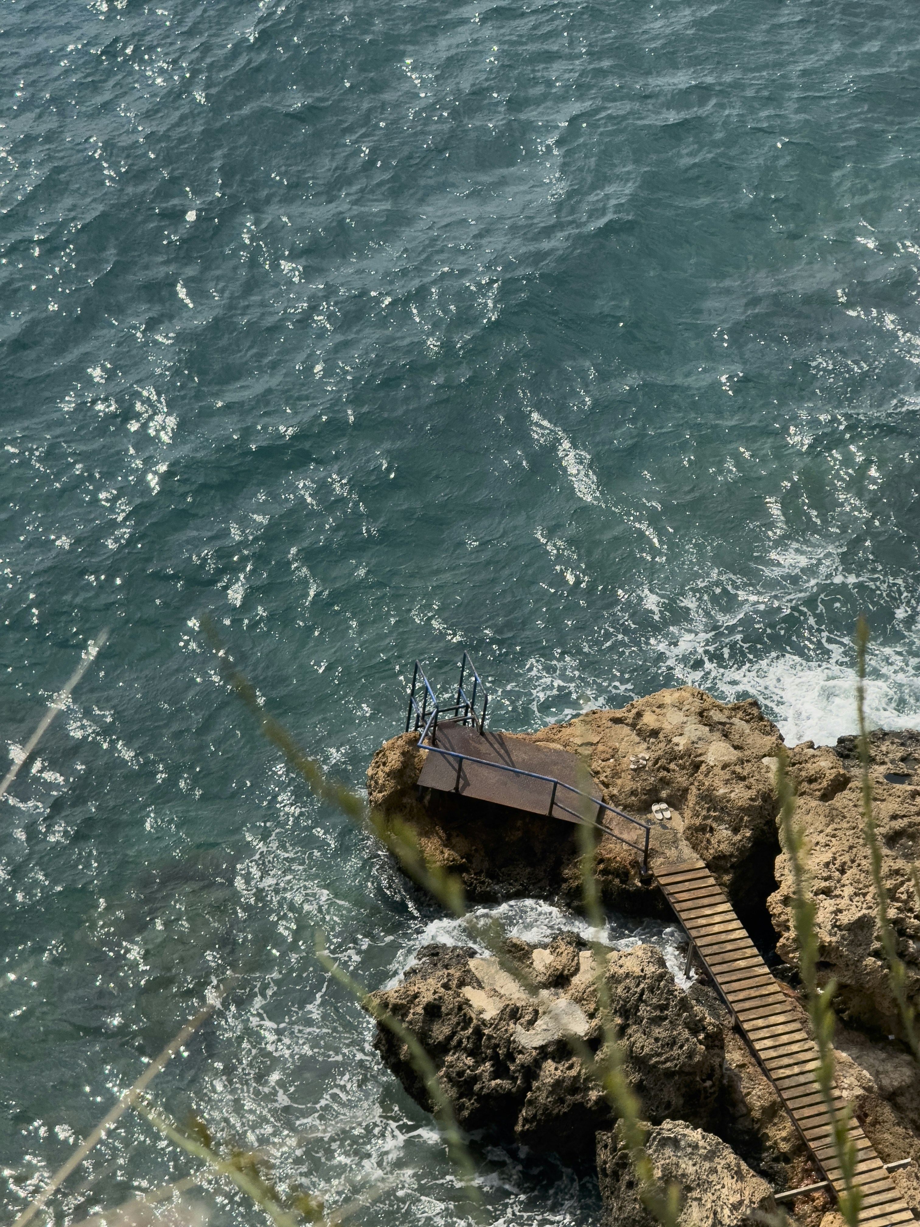rocky seaside staircase | Wooden steps lead to a platform on a rocky cliff by the sea.