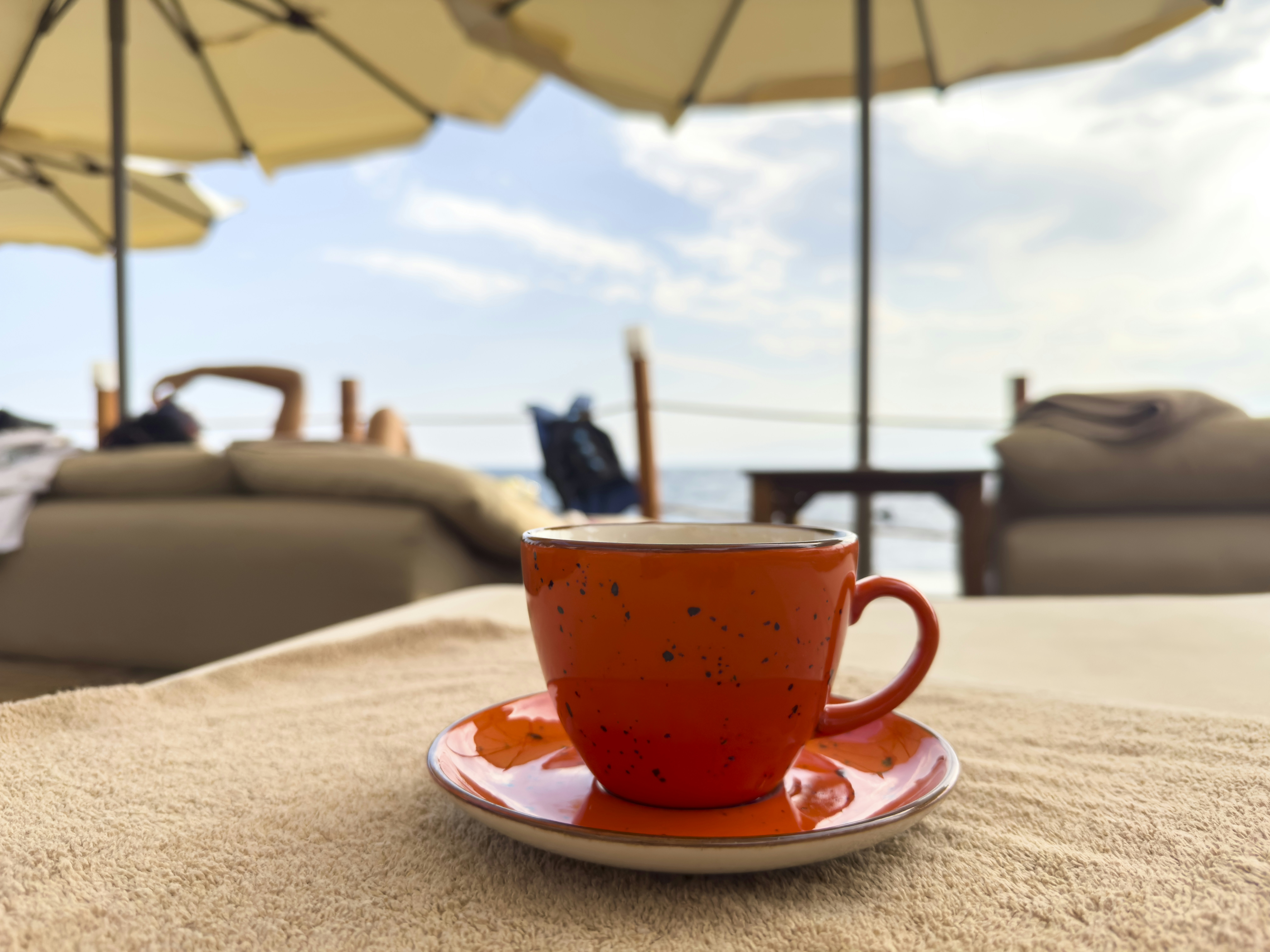 close-up of coffee by the sea | Orange cup of coffee on beach lounge chair