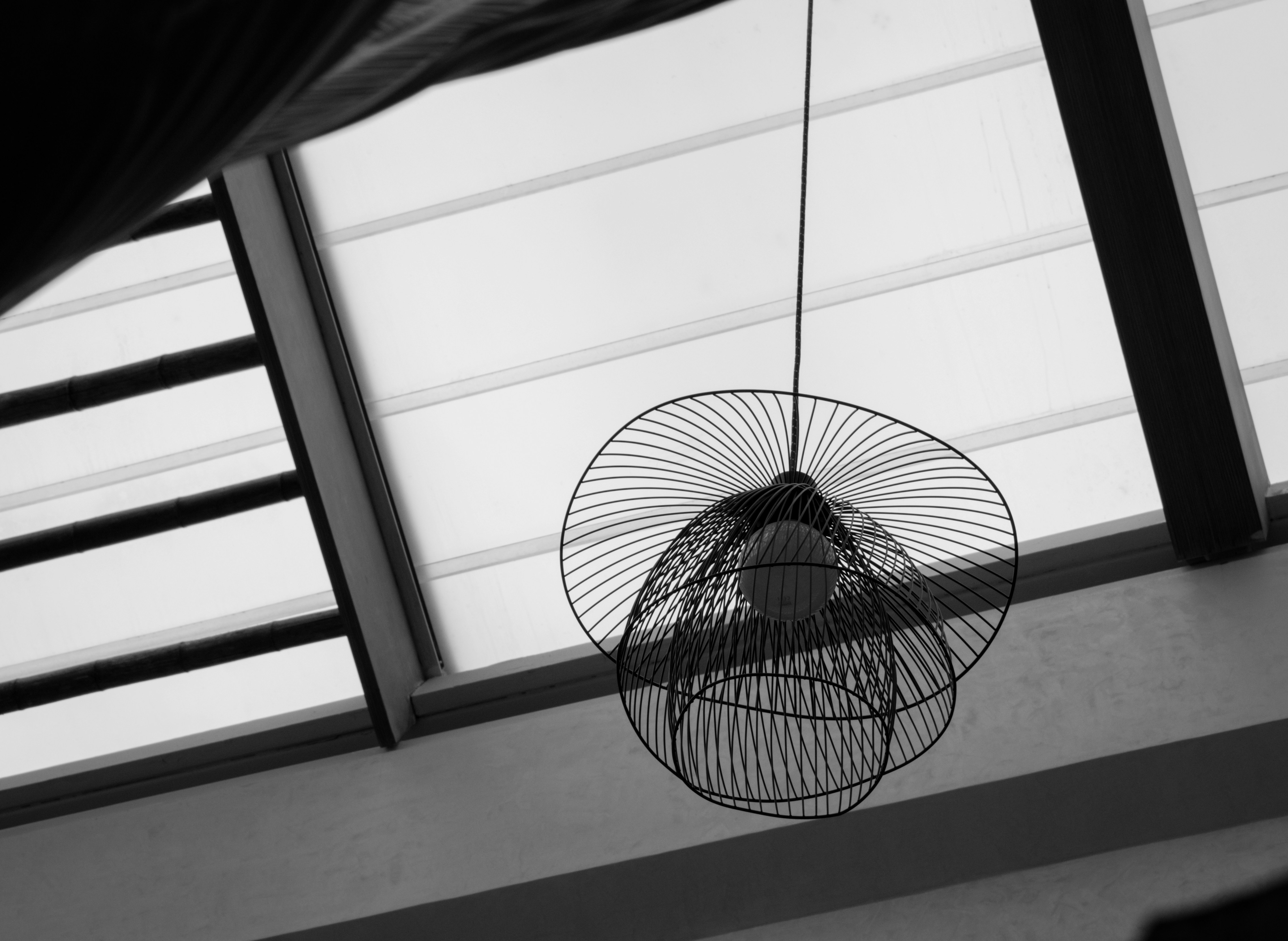 black-and-white photo of a ceiling with a skylight. A modern wire-frame pendant light hangs from the center, showing a circular and layered design. | Modern wireframe chandelier hanging from ceiling