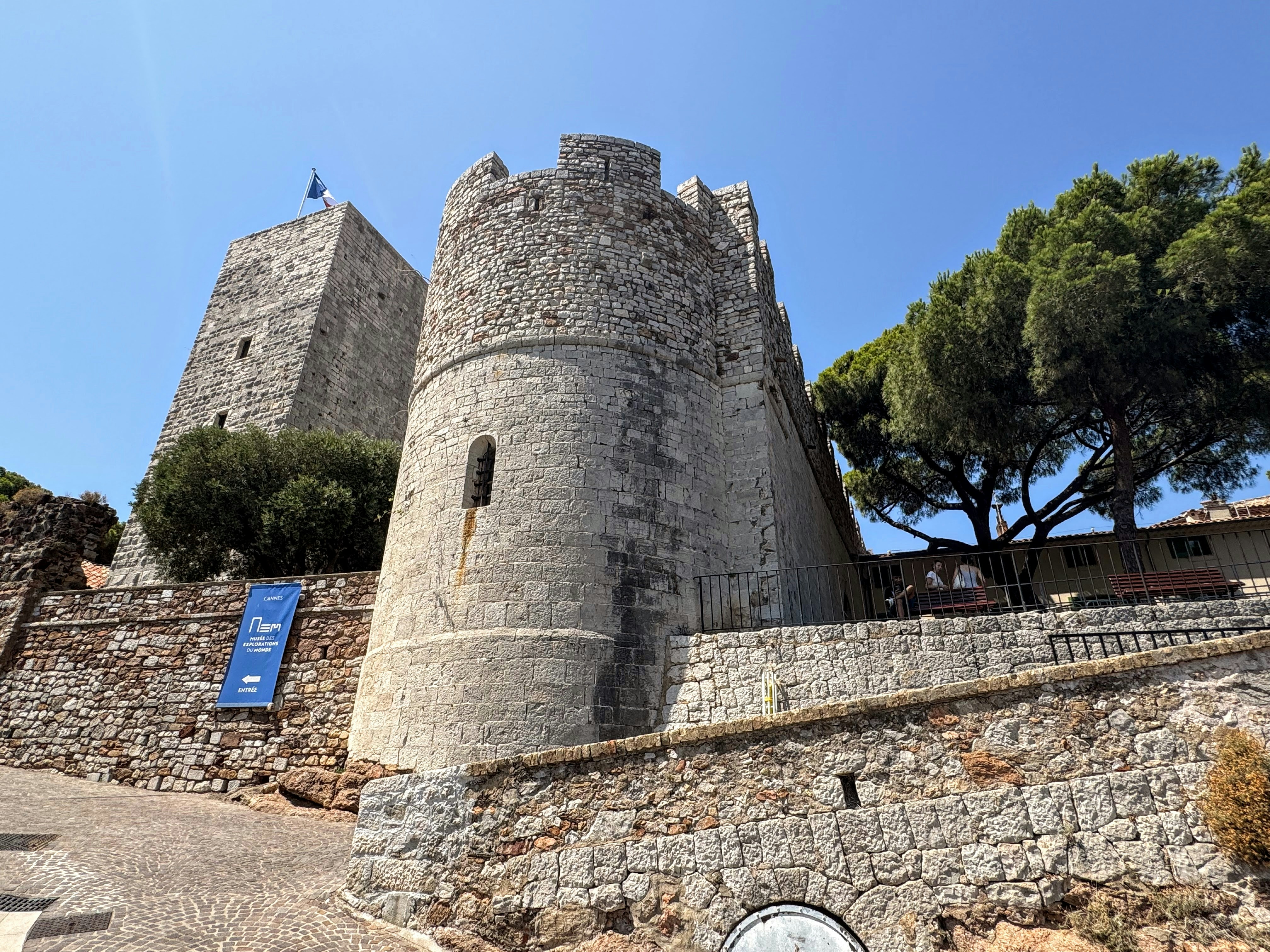 Ancient stone fortress with a round tower, surrounded by lush greenery and a clear blue sky. A historical site reflecting architectural resilience.