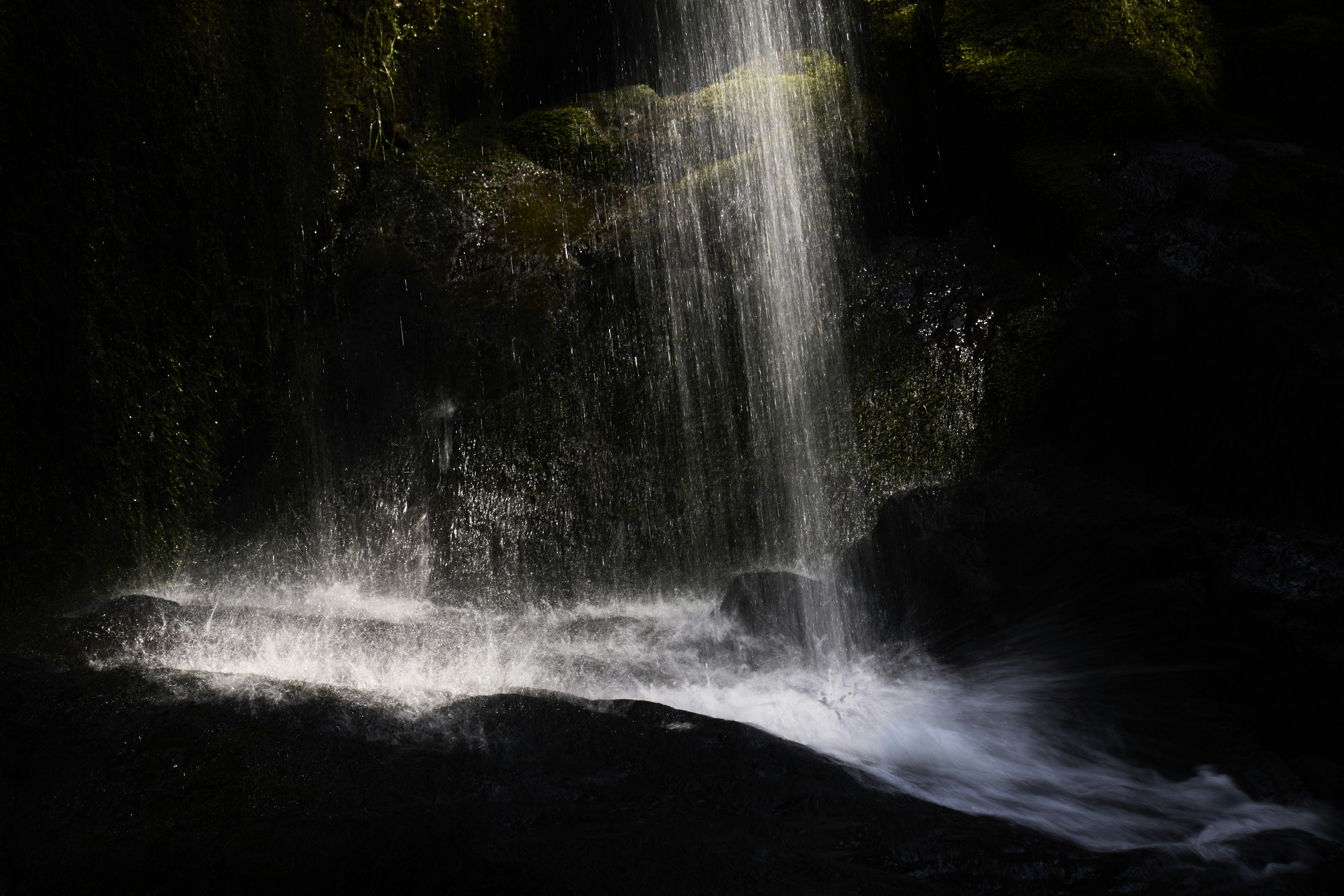 Water cascading down a rocky surface, creating a misty spray in a darkened forest setting.