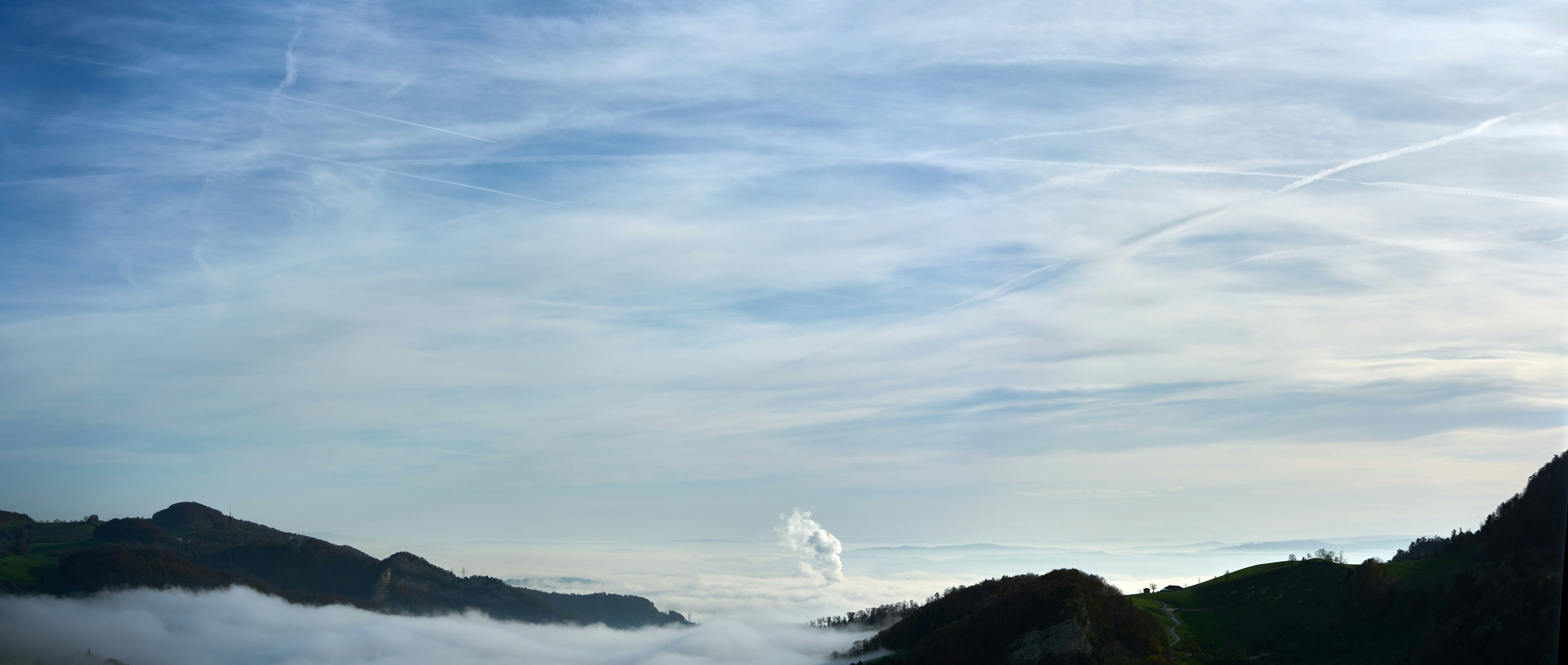 A serene landscape where rolling hills meet a blanket of fog, with wisps of clouds stretching across a gentle sky. The scene evokes a sense of tranquility.