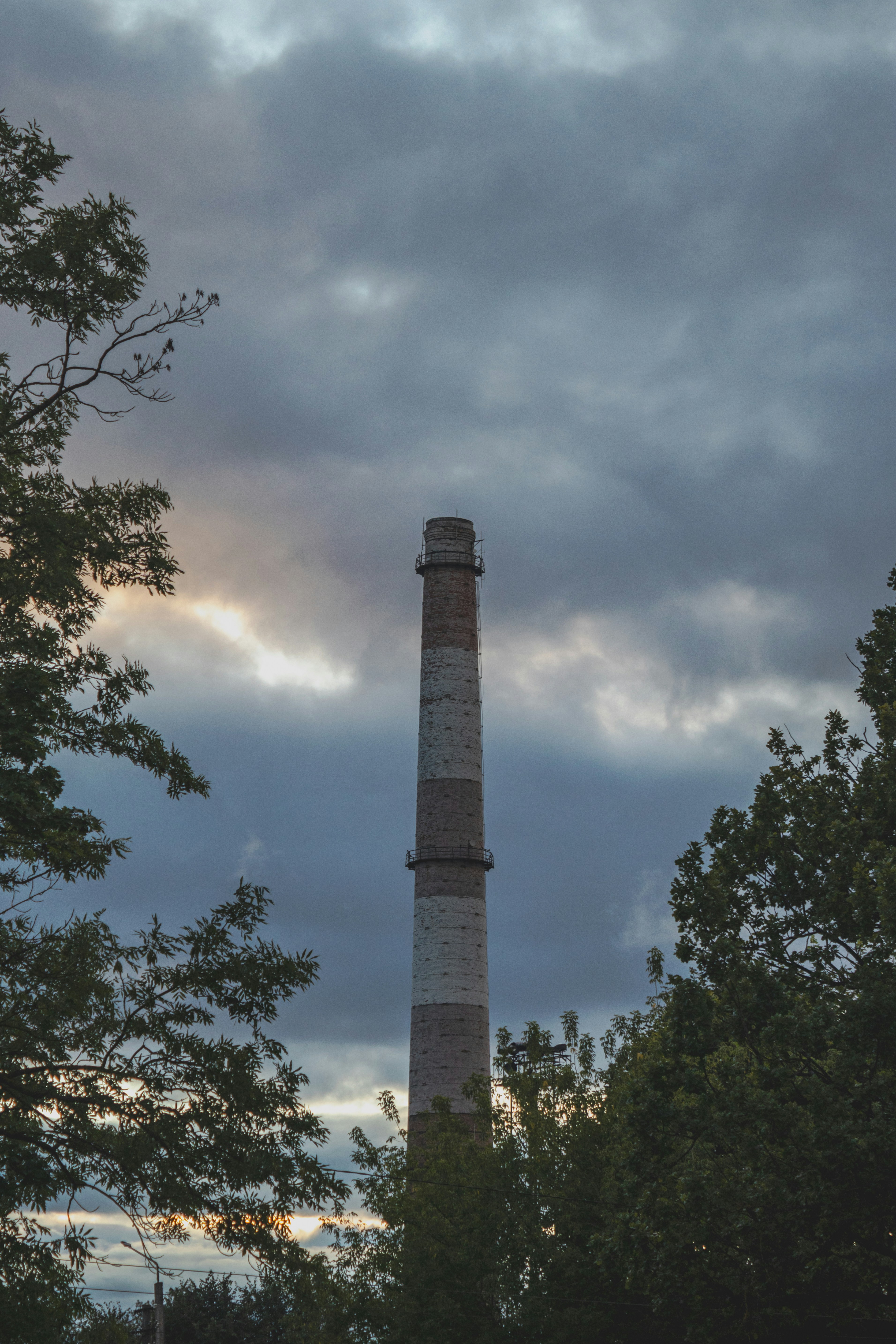 Industrial brick chimney on a cloudy day. | Tall industrial chimney against a cloudy sky