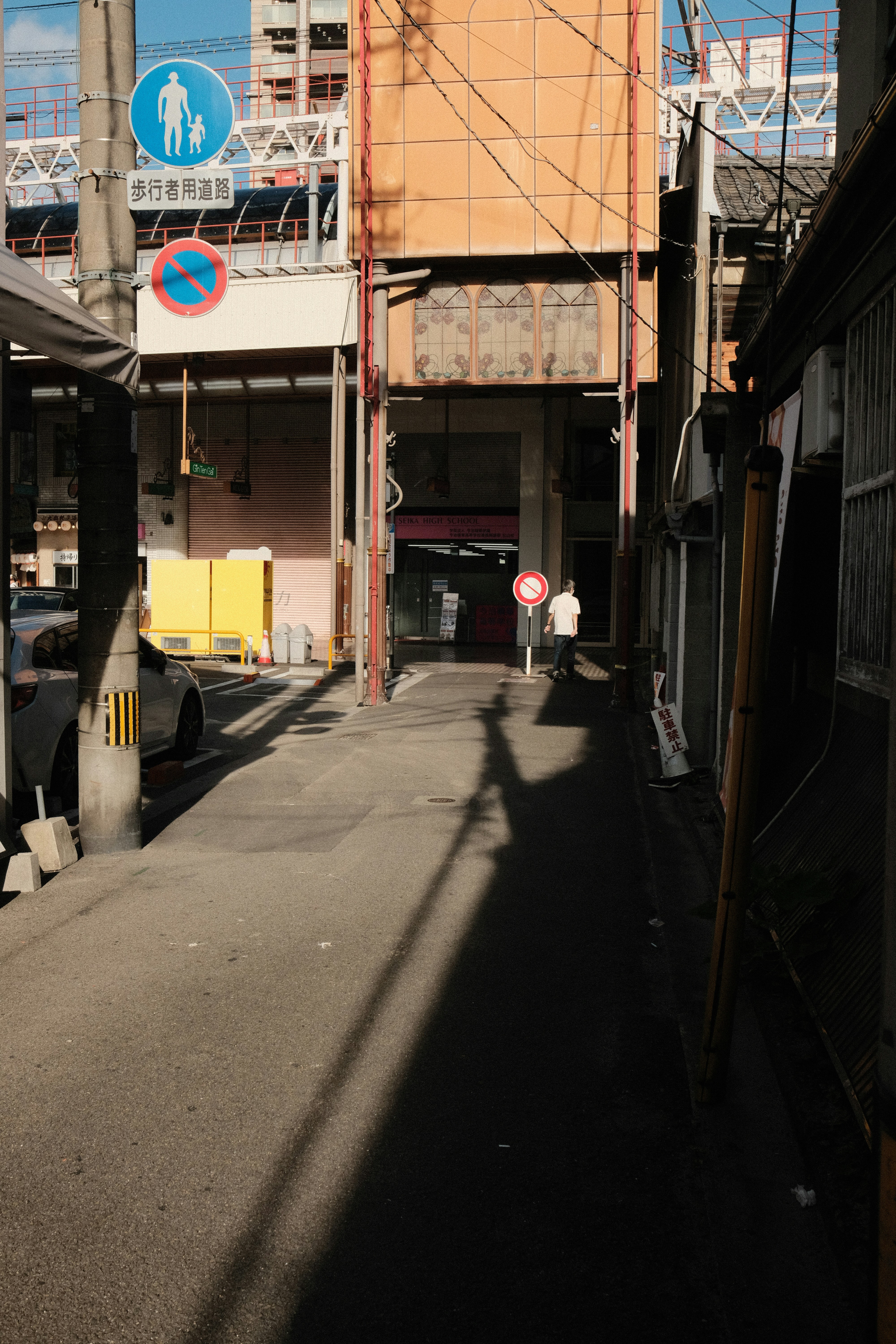 Man walks down a narrow urban alleyway with shadows.